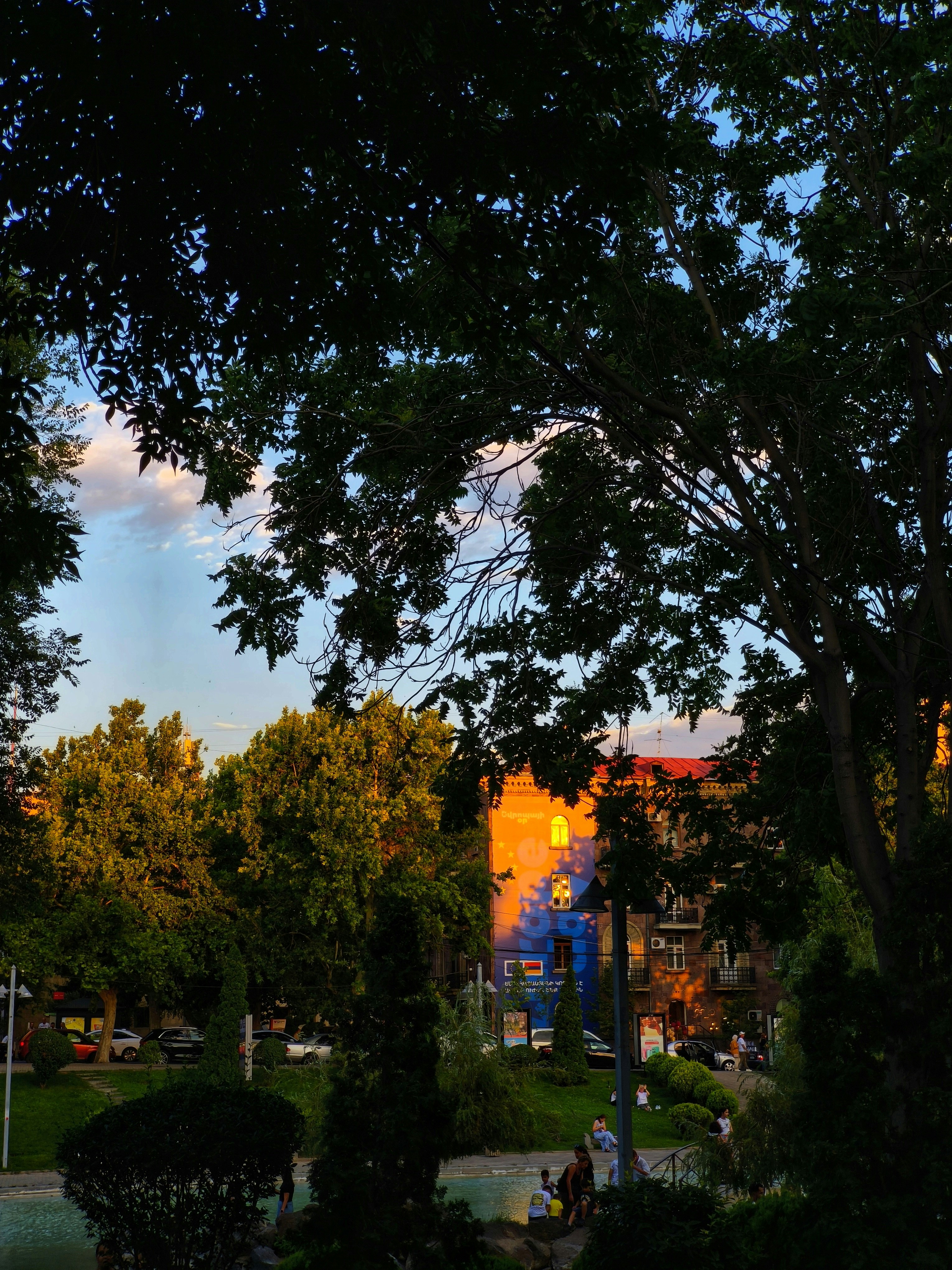 A beautiful view of the Swan lake in the center of the capital of Armenia, Yerevan | Sunset illuminates a building through trees.