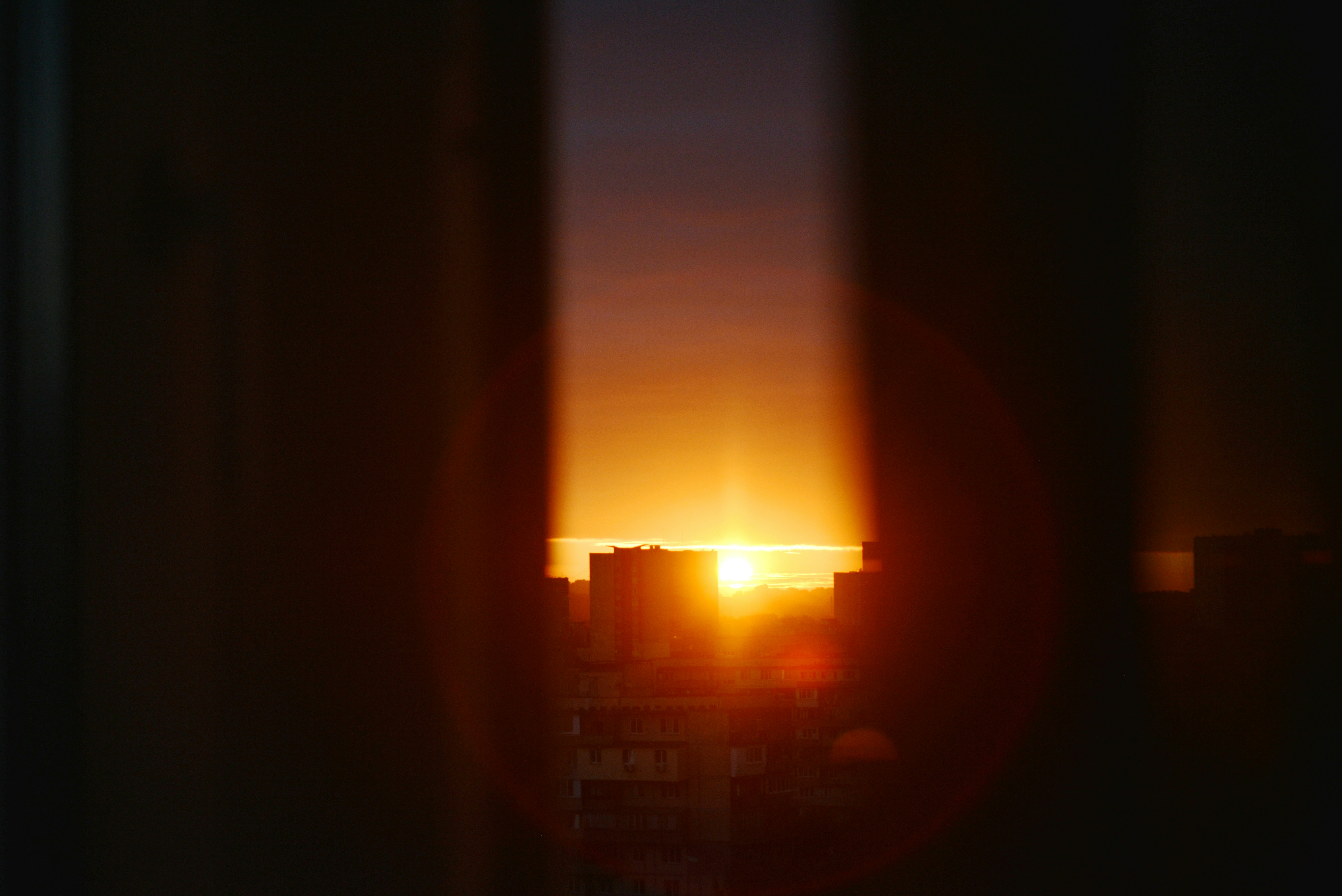 Sunrise over a city, framed by curtains.