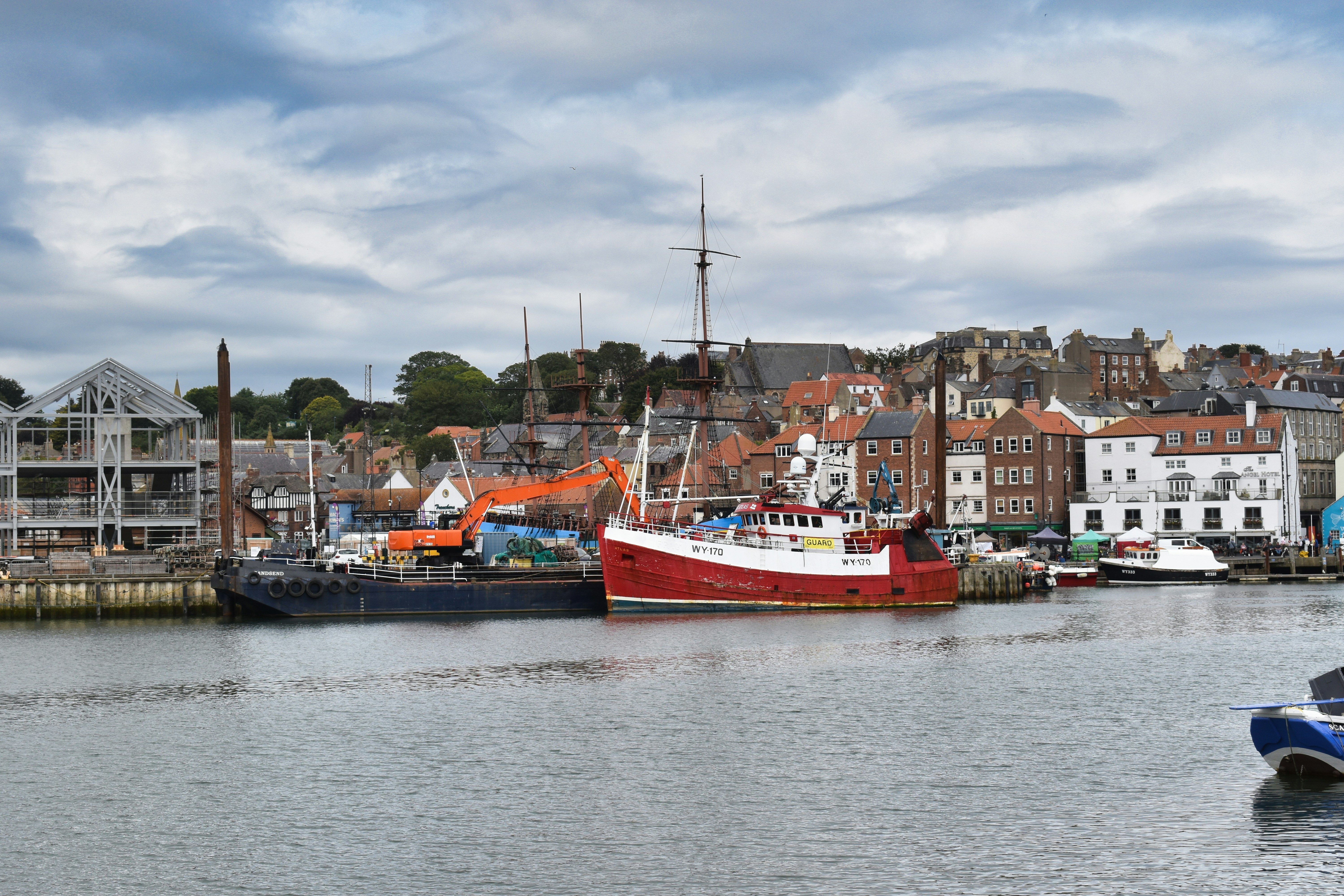 Vibrant fishing boats docked in a bustling harbor with historic buildings in the background. The scene captures the blend of maritime activity and coastal charm.