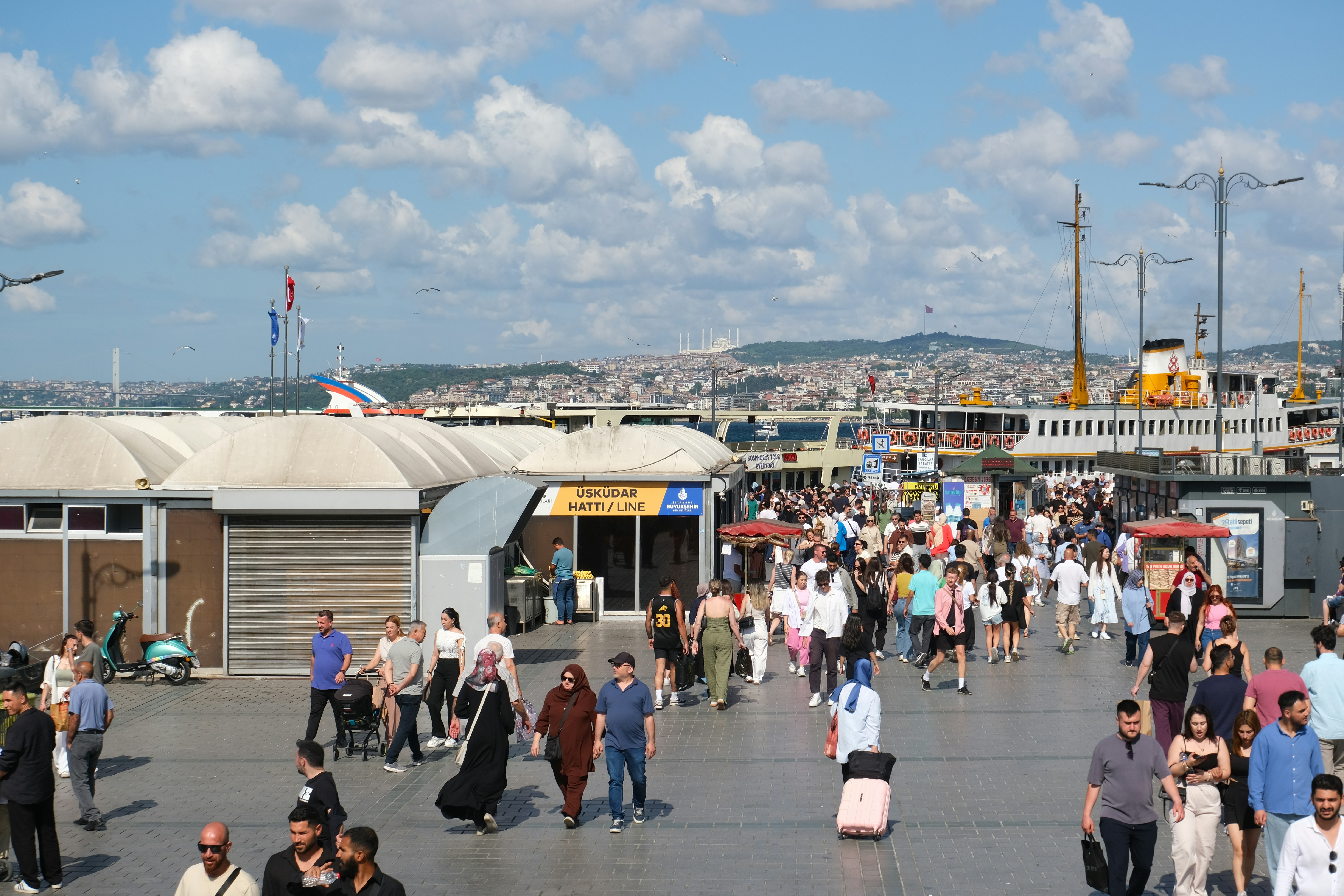 Crowds of people walk along a sunny city harbor.