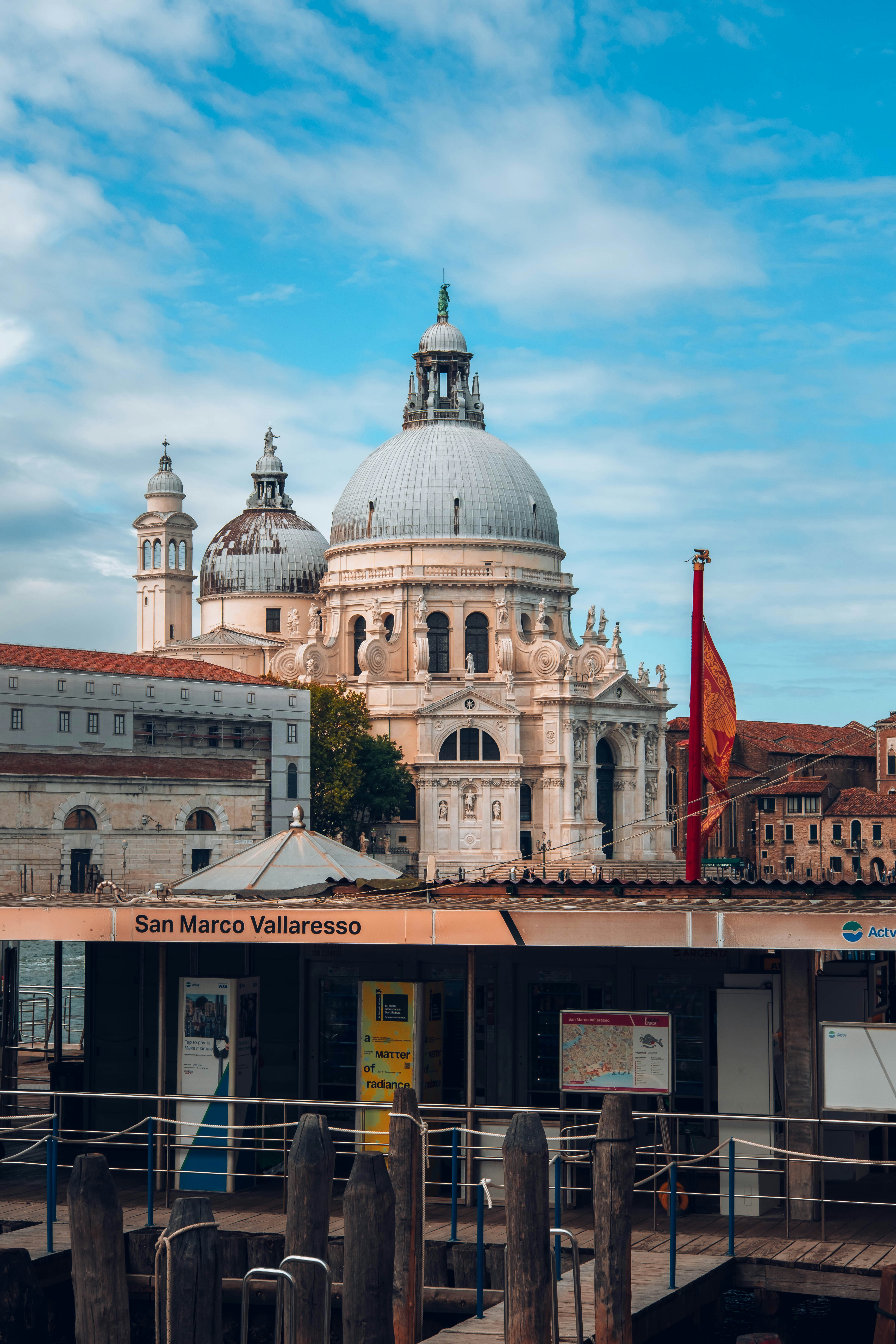 Historic architecture of San Marco Vallaresso with a backdrop of iconic domes and a vibrant flag. The scene captures the essence of Venice's rich cultural heritage.