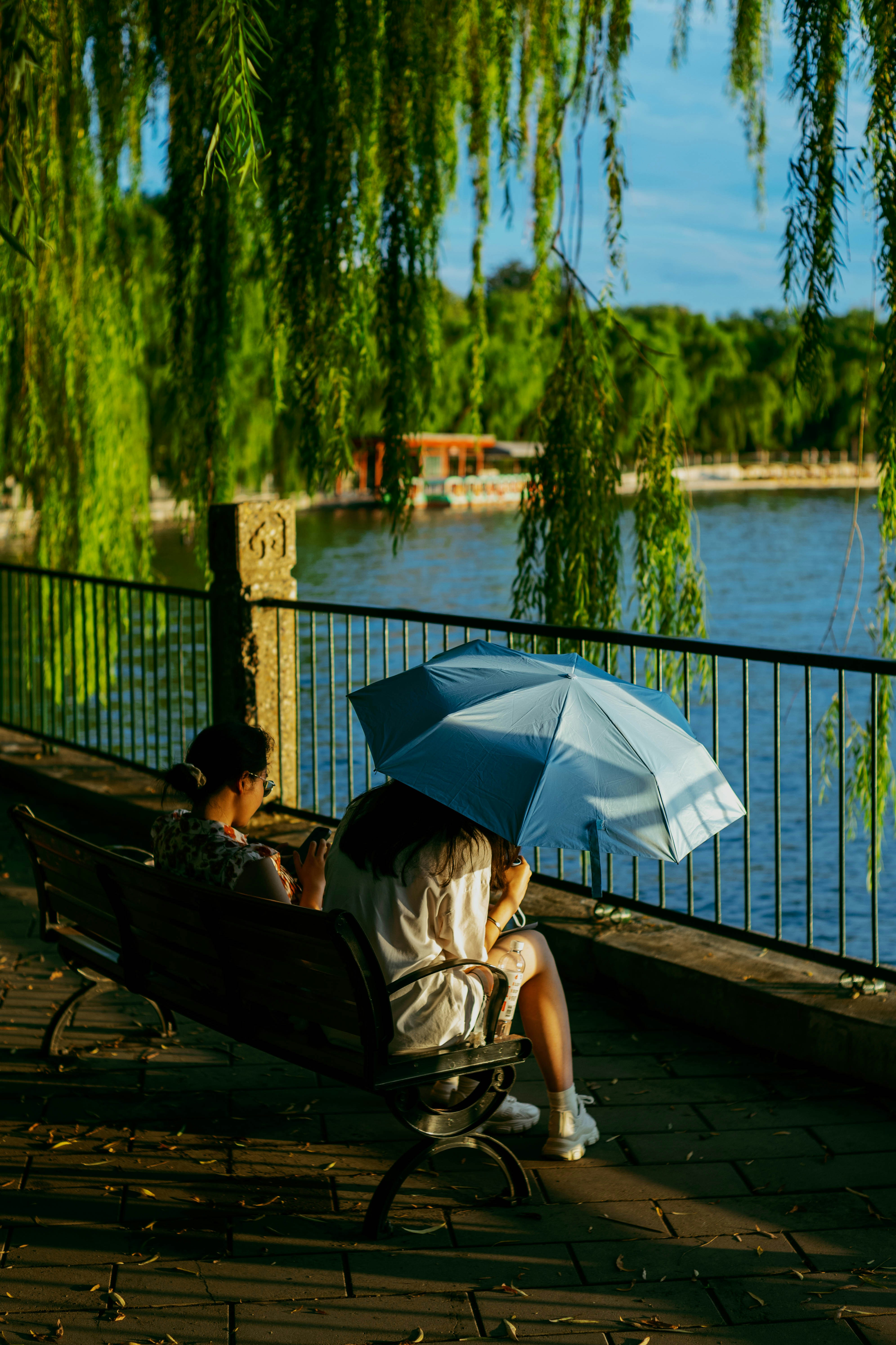 Two people sit under an umbrella near a lake.