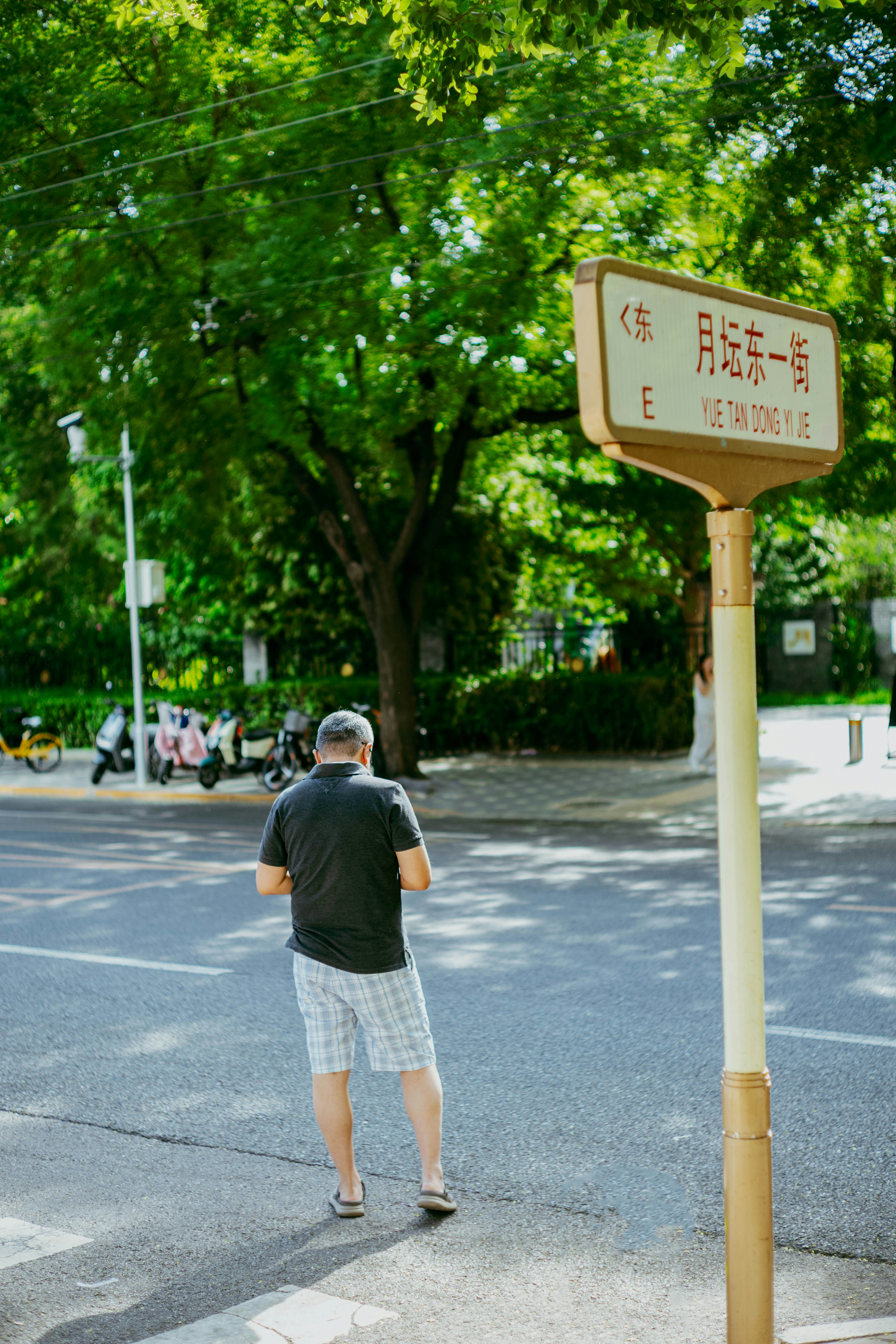 A man stands near a street sign in the sun.
