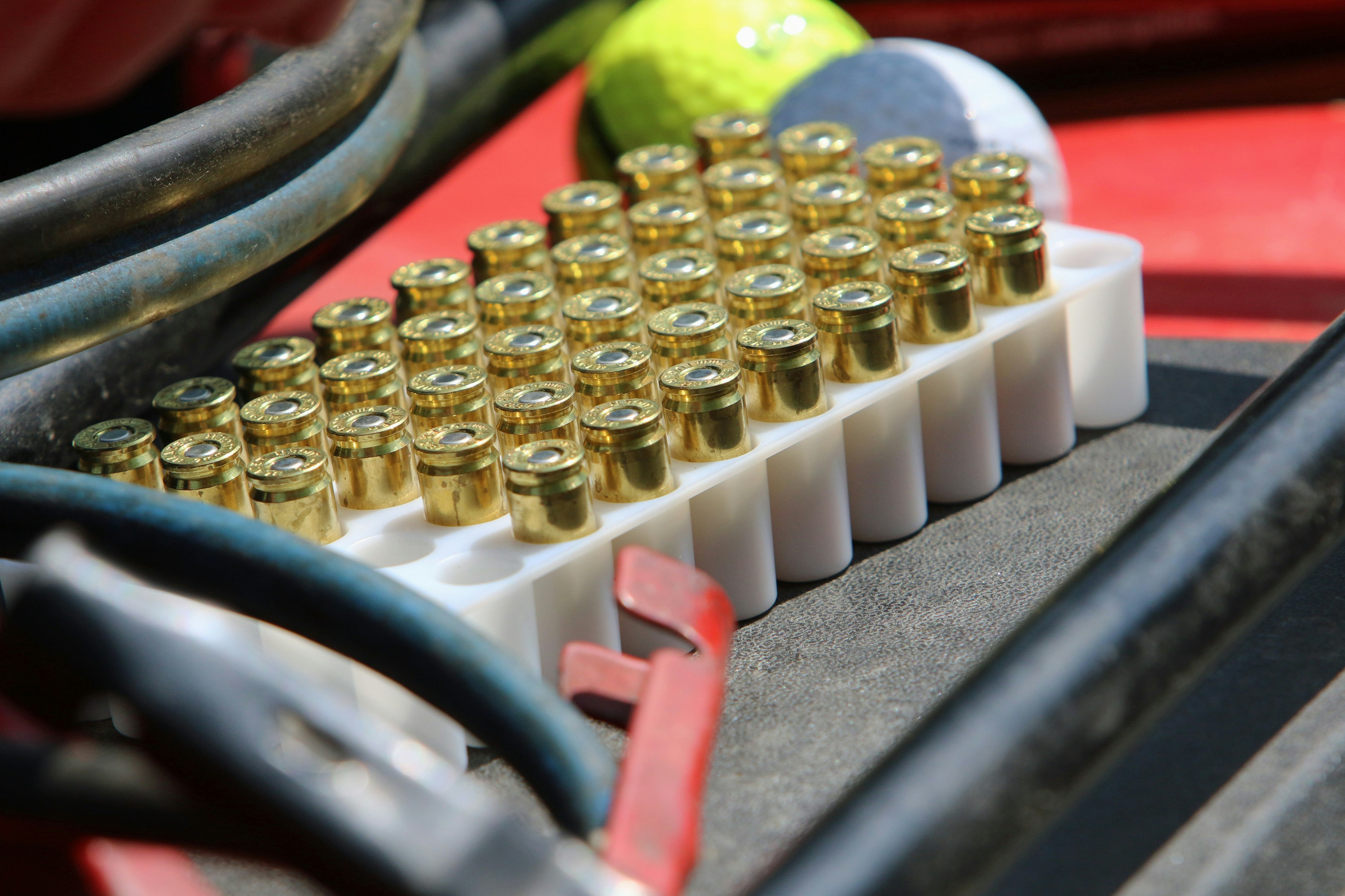 A neatly arranged tray of brass ammunition shells rests on a work surface, surrounded by tools and golf balls, showcasing a blend of precision and leisure.