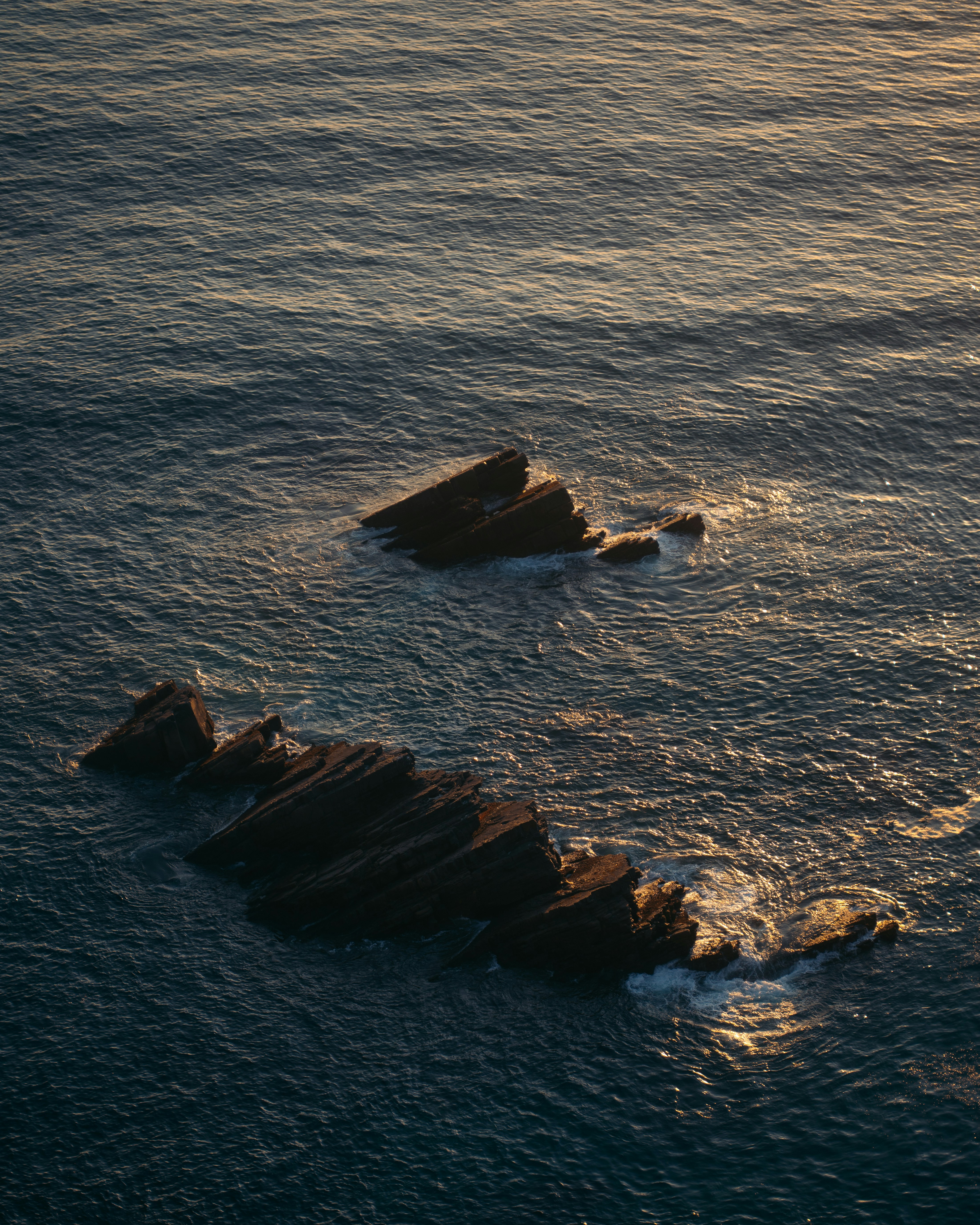Rocks emerge from a calm ocean's surface.