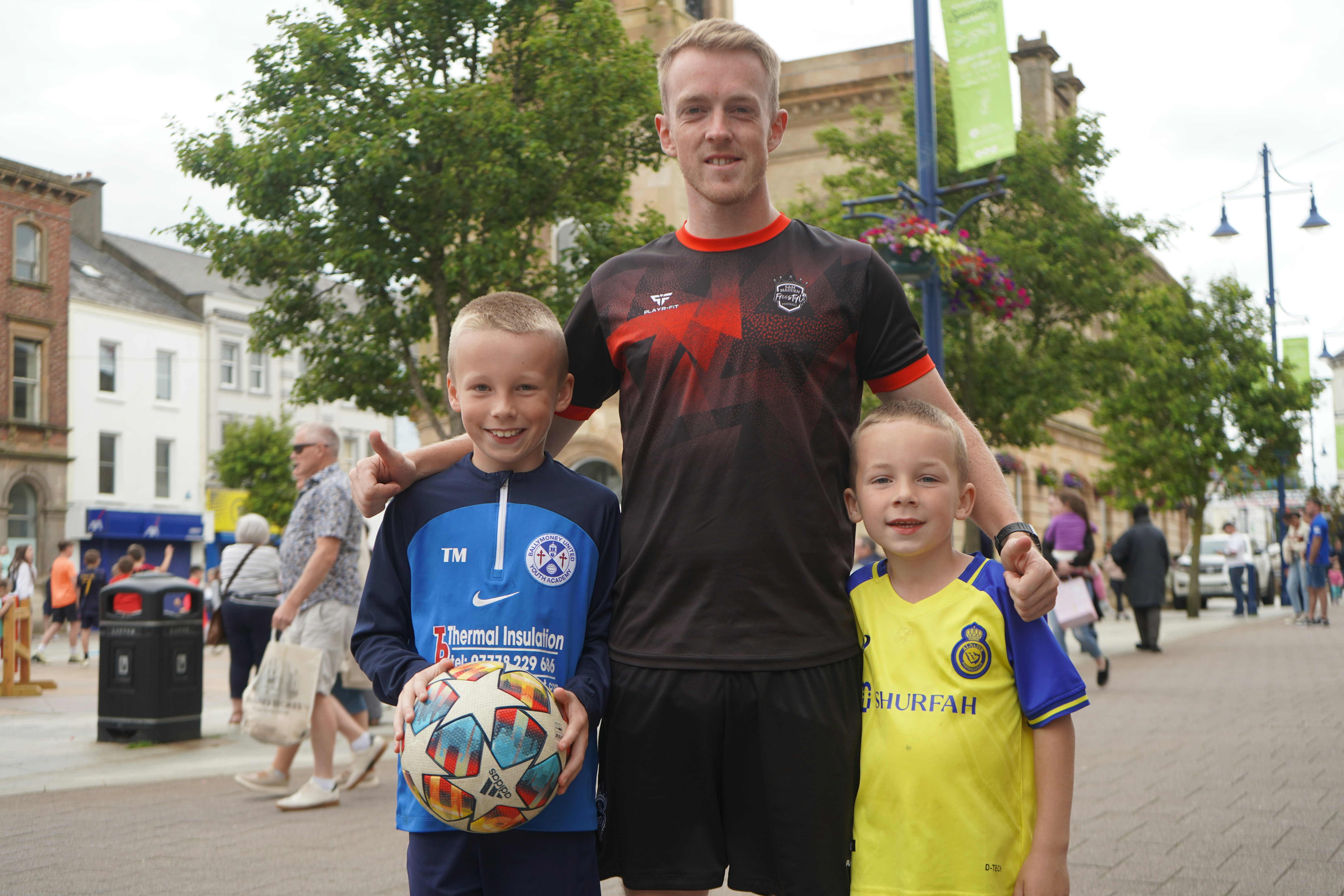 Center-Stage Trio: A Father and Two Boys Share a Sunlit Street Football Moment