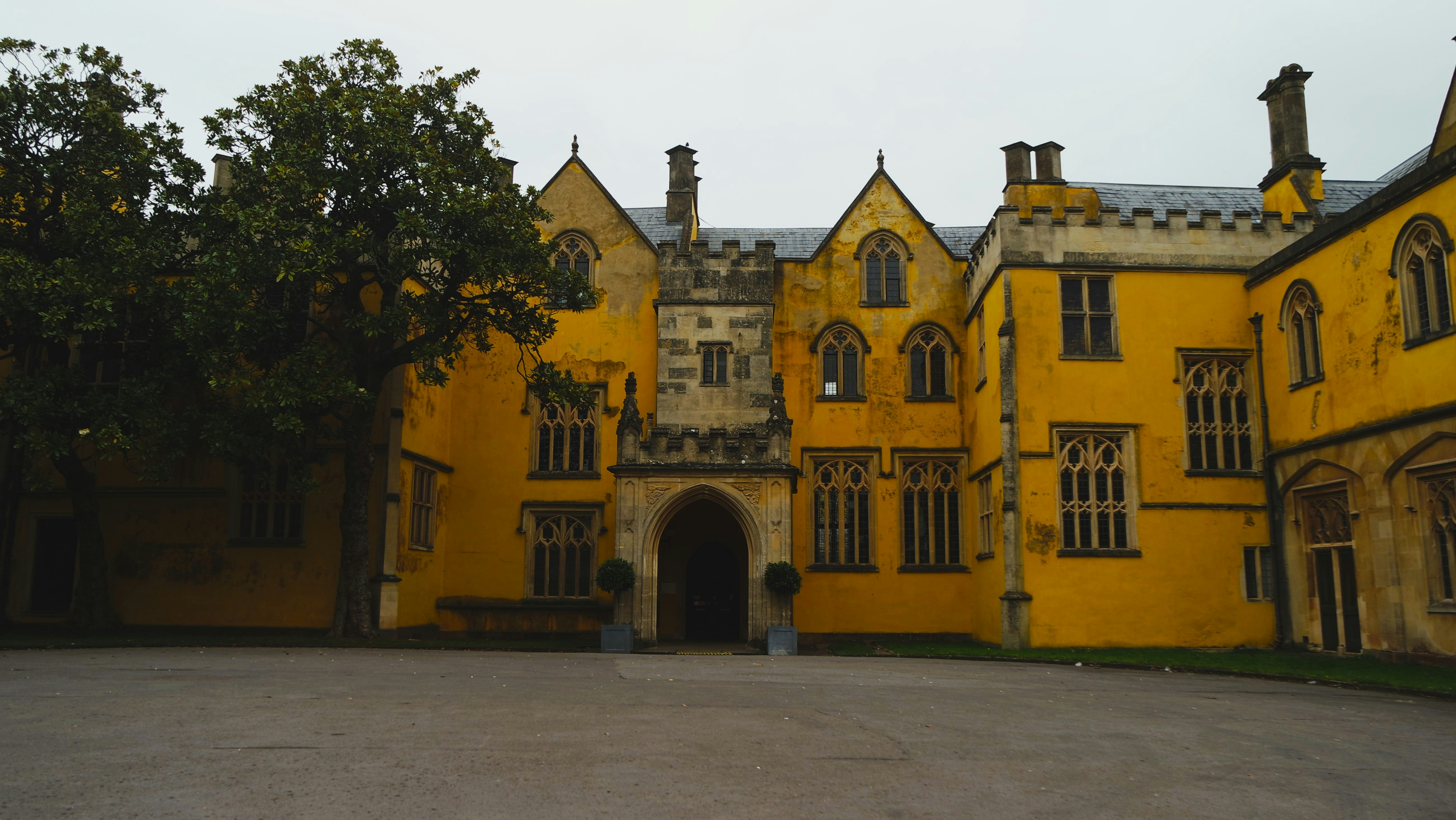 Historic yellow mansion showcasing intricate architecture and tall windows, framed by lush greenery. A grand entrance invites exploration.