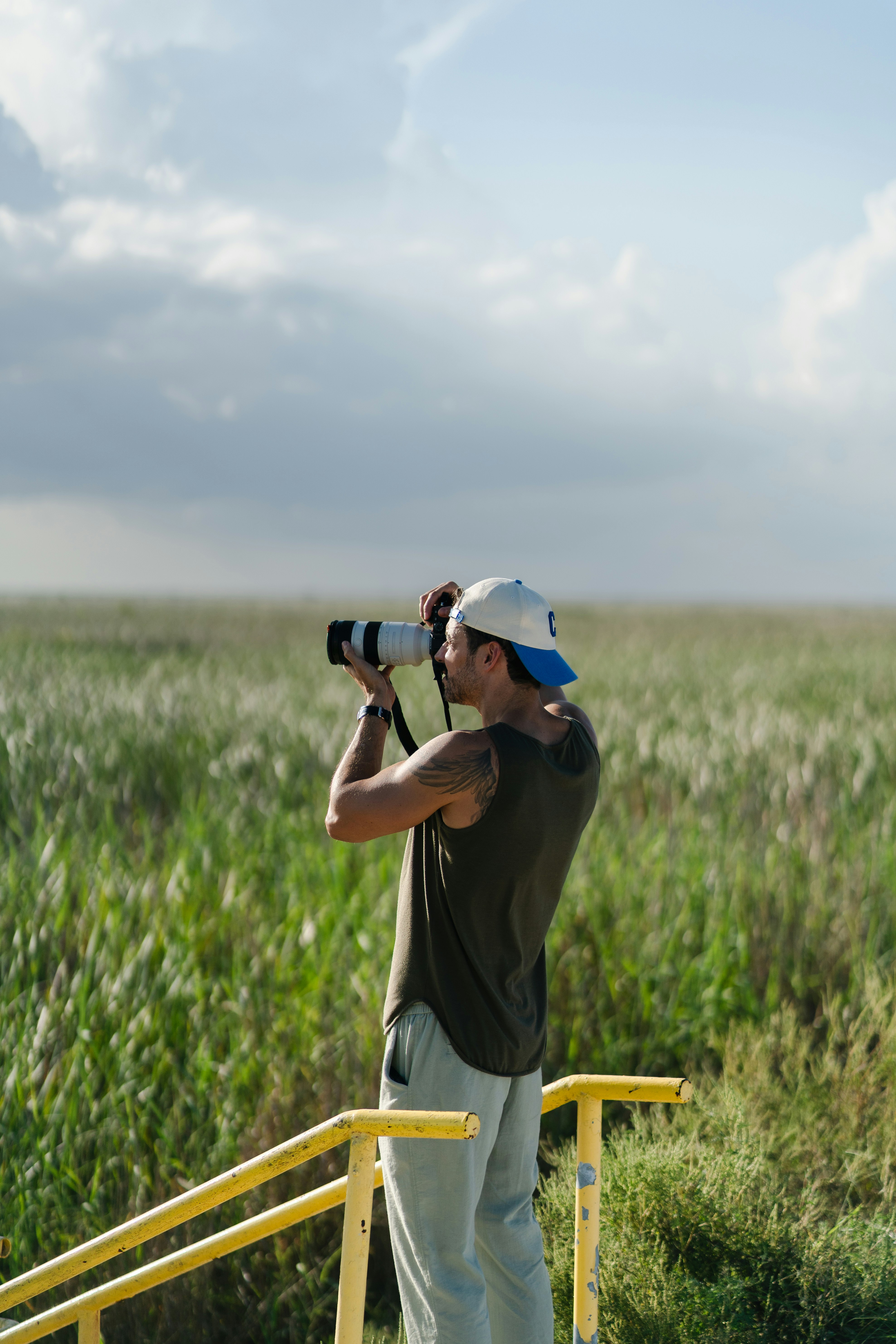 Photographer capturing the serene landscape with a telephoto lens, framed by lush grass and a cloudy sky.