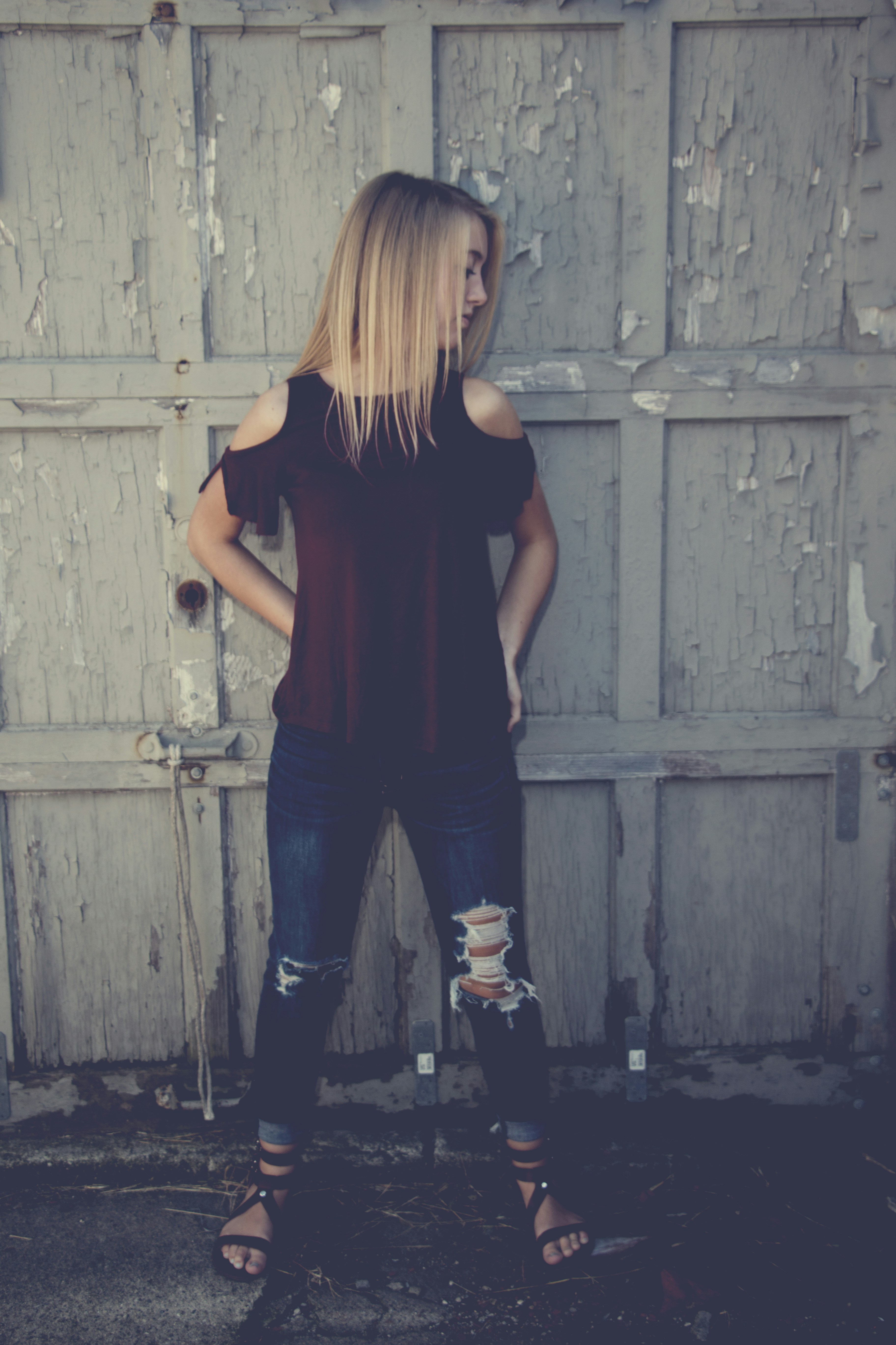 old garage door, garage door, girl, ripped jeans, old building | A young woman poses in front of a door.