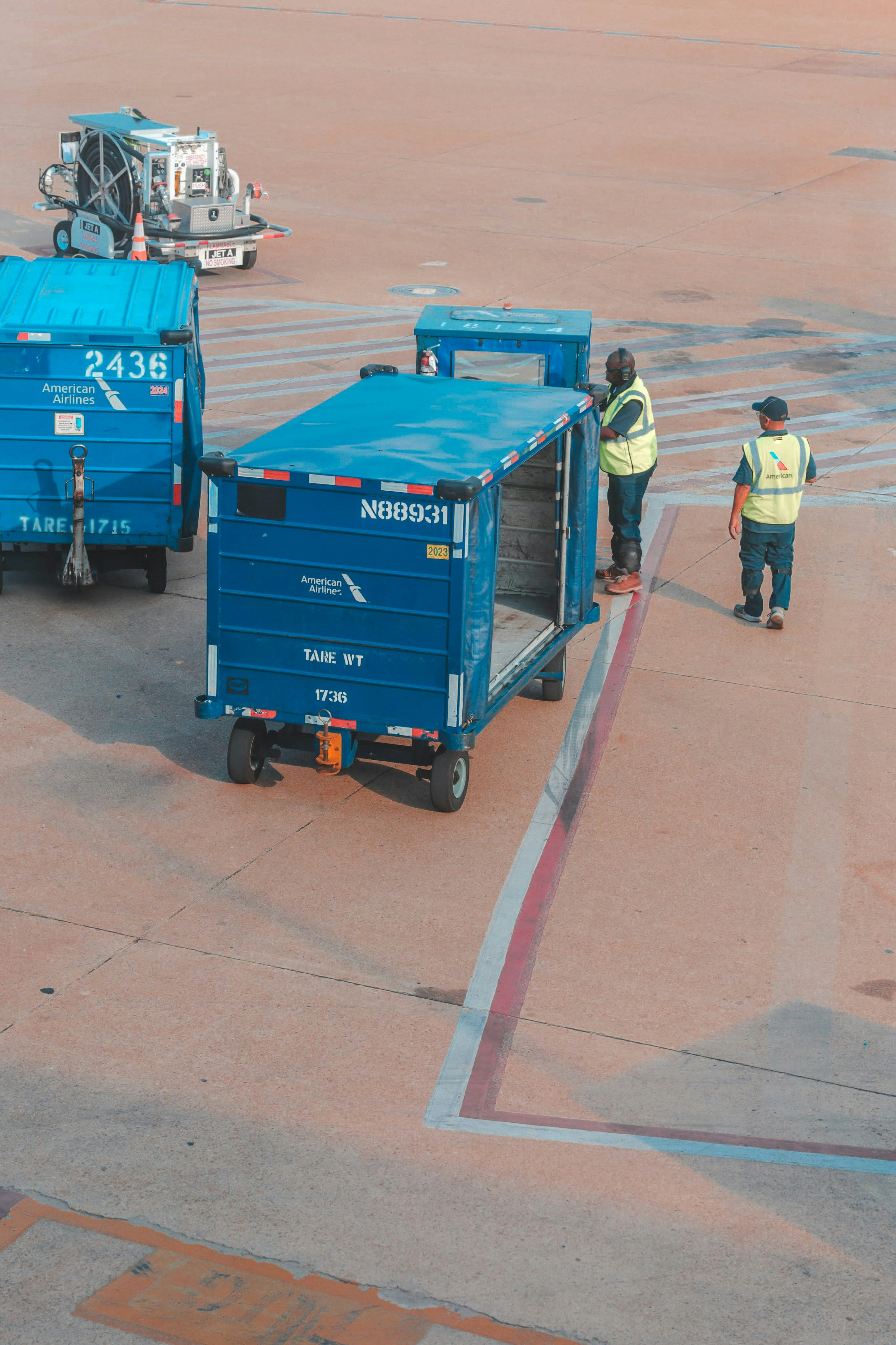 Two airport personnel manage cargo containers on the tarmac, showcasing the logistical efforts behind air travel.