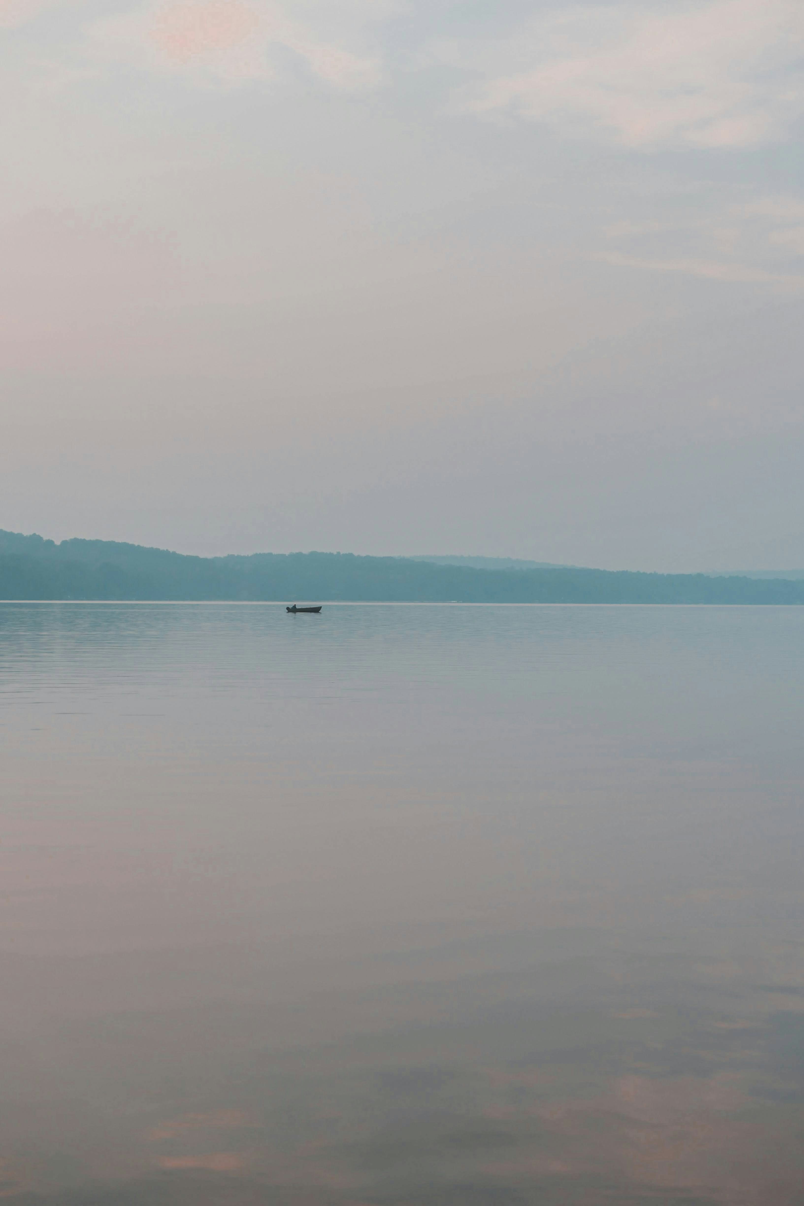Calm lake with a distant boat under a cloudy sky.