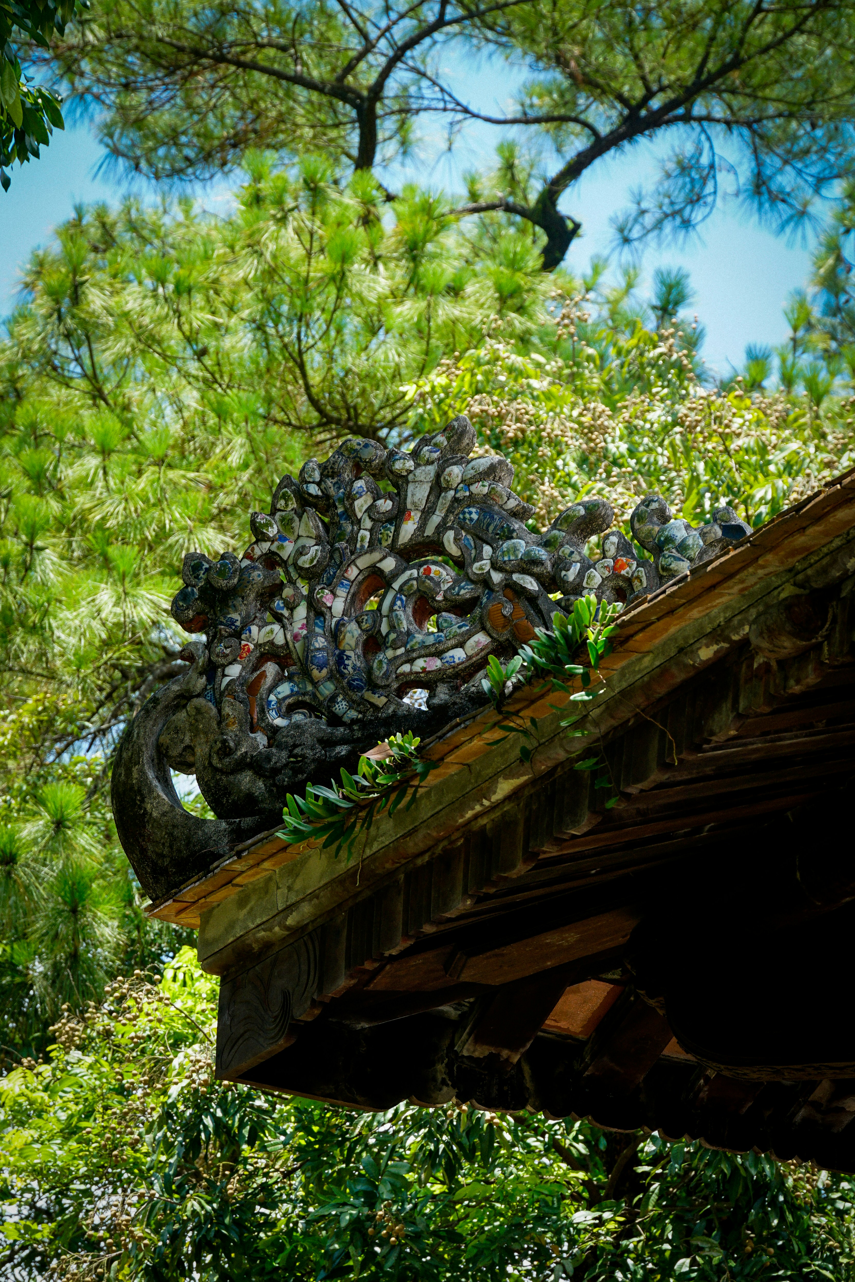 Intricately carved roof ornamentation adorned with vibrant colors, framed by lush greenery and dappled sunlight.