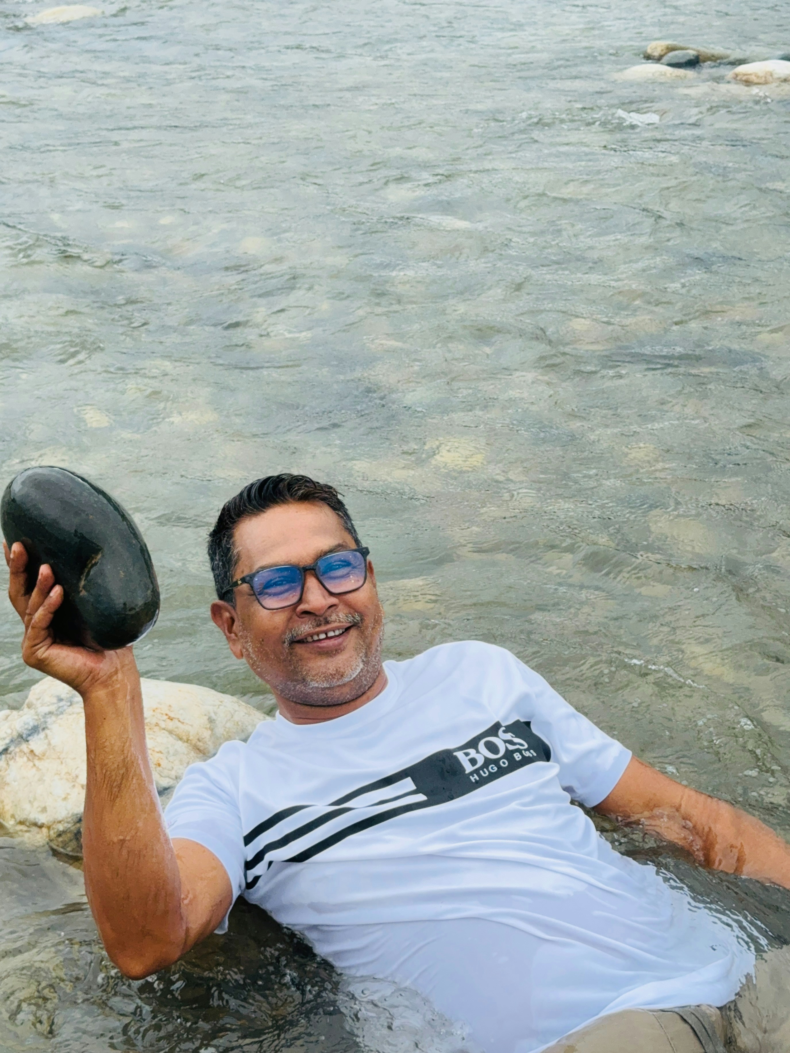 Shallow Waters, Bright Smile: A Man Lifts a Stone in Sunny Shallows