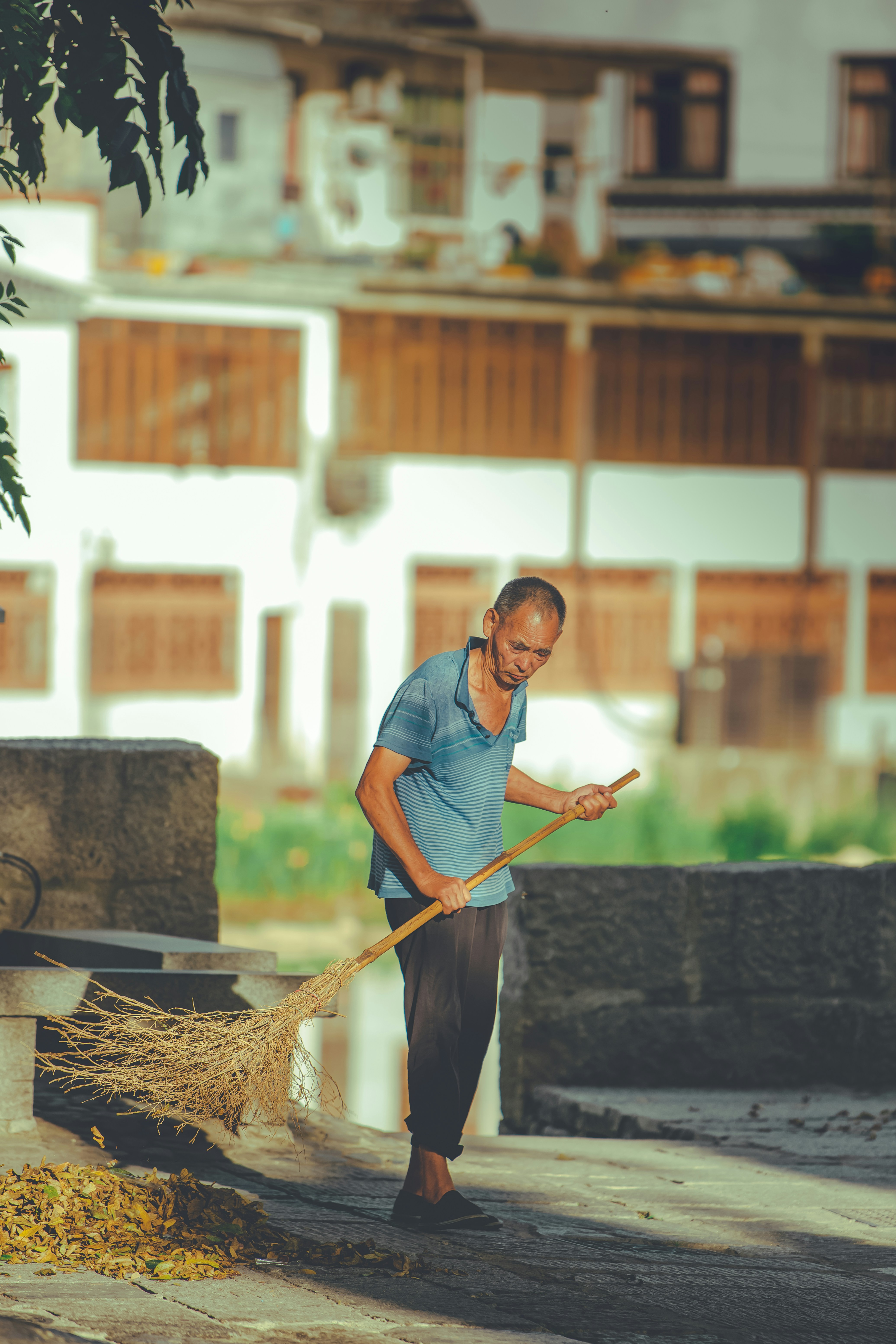 The old man sweeping the street. | A man sweeps the street in a small town.