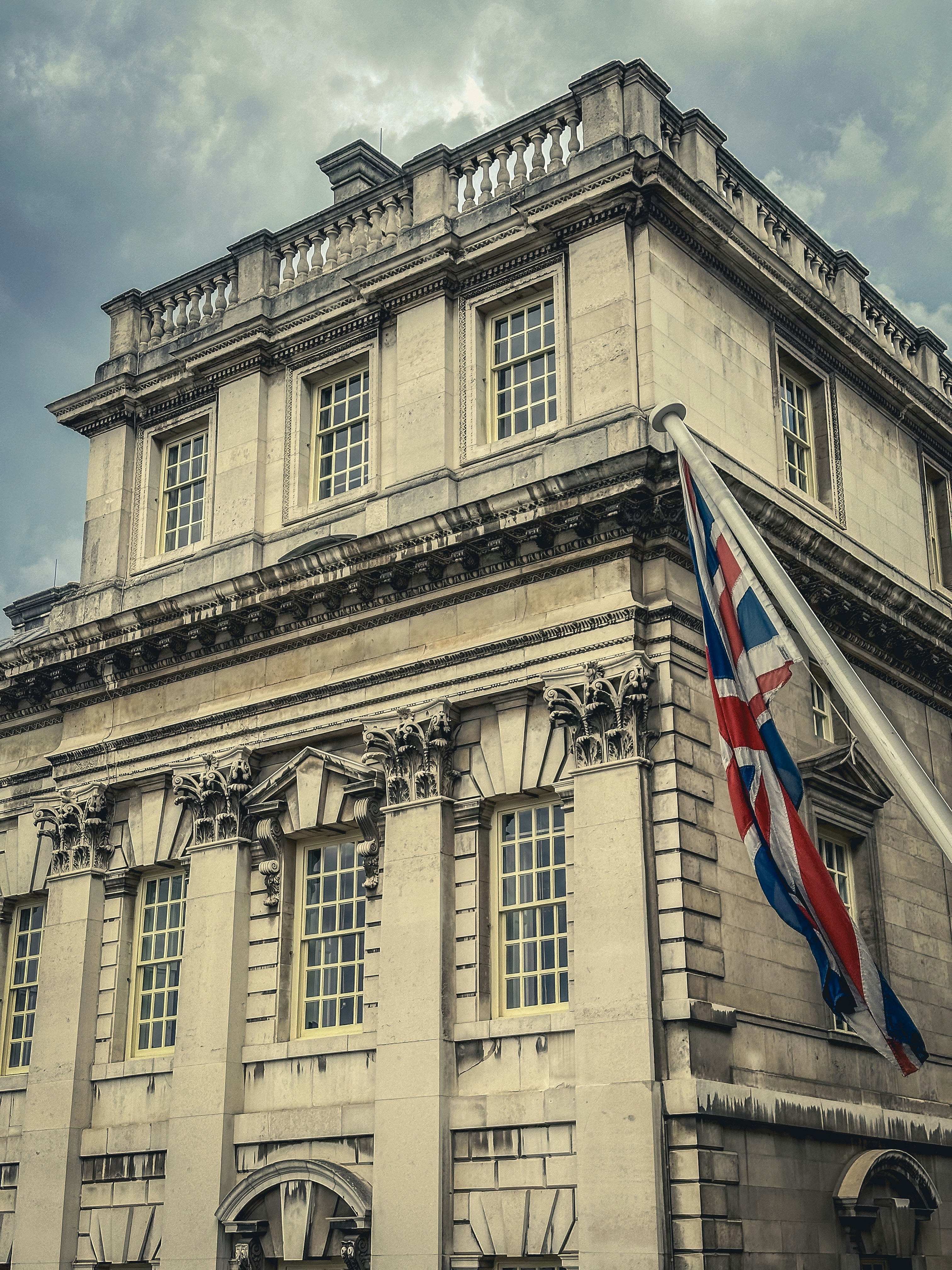 Historic building adorned with intricate architectural details and a waving Union Jack flag under a moody sky.