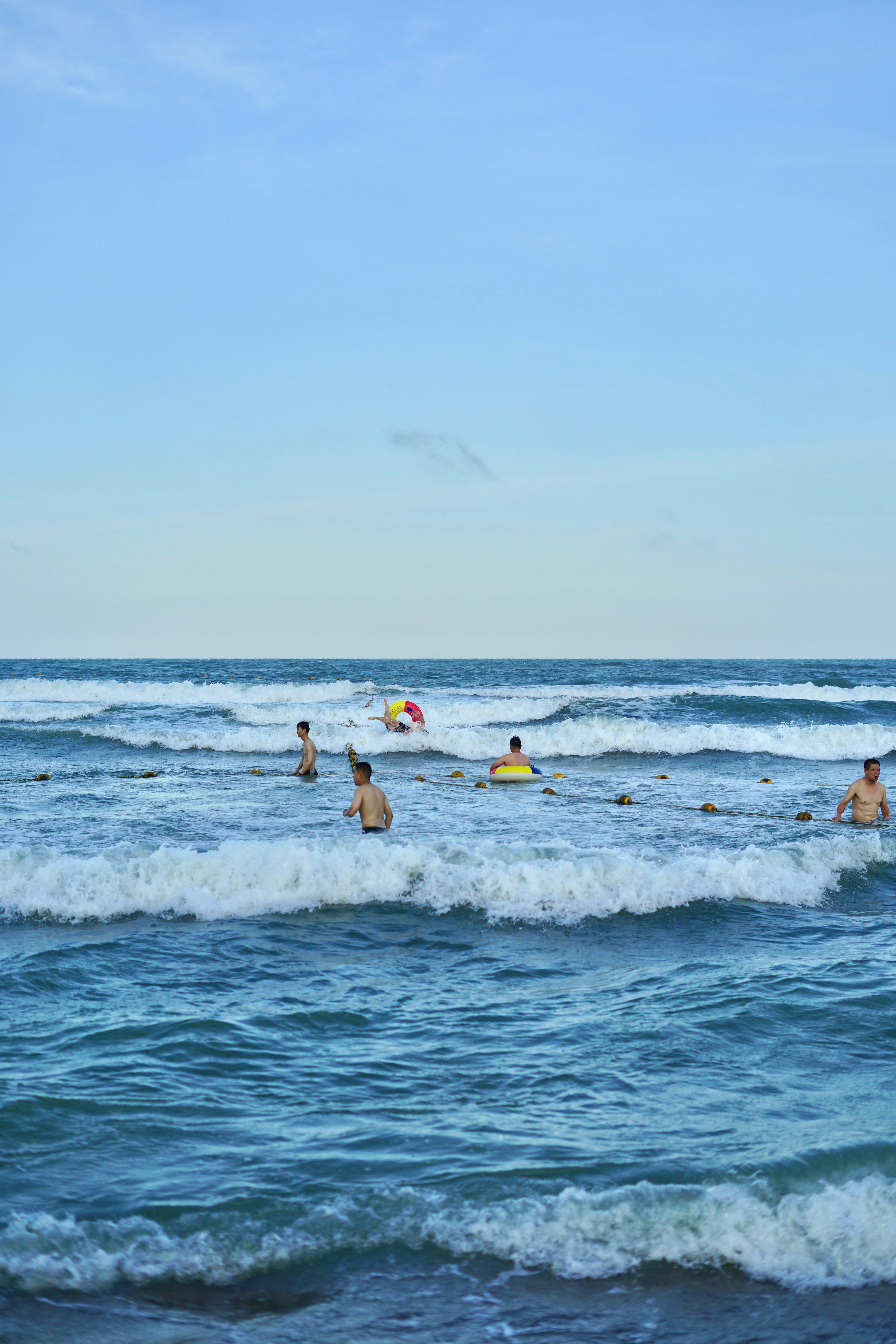 Individuals enjoying a sunny day in the ocean, surrounded by gentle waves and a beach ball. The scene captures the essence of summer leisure.