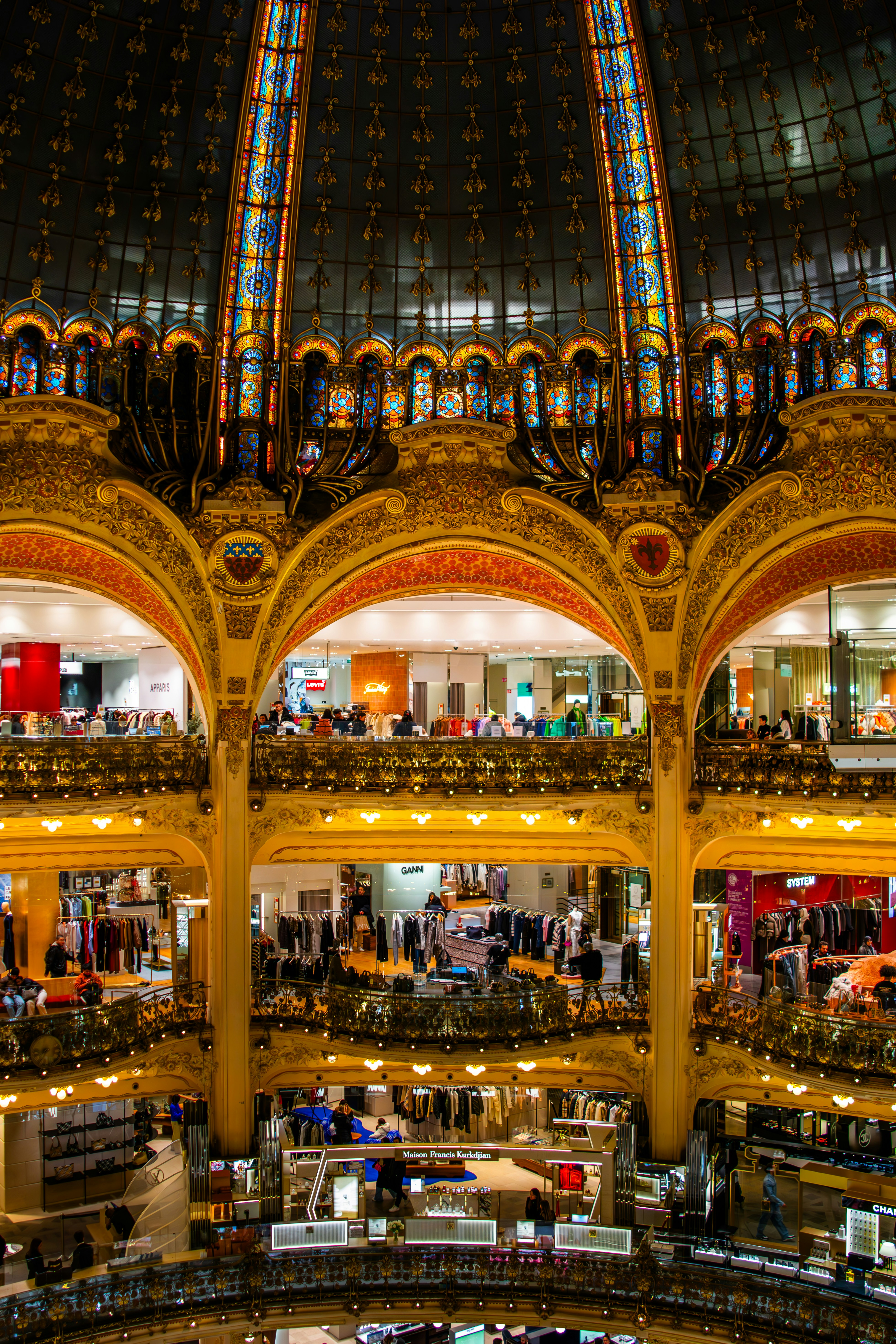 Intricate architectural details of a grand shopping center, showcasing multiple levels filled with boutiques and shoppers. The ornate ceiling adds a touch of historical charm.