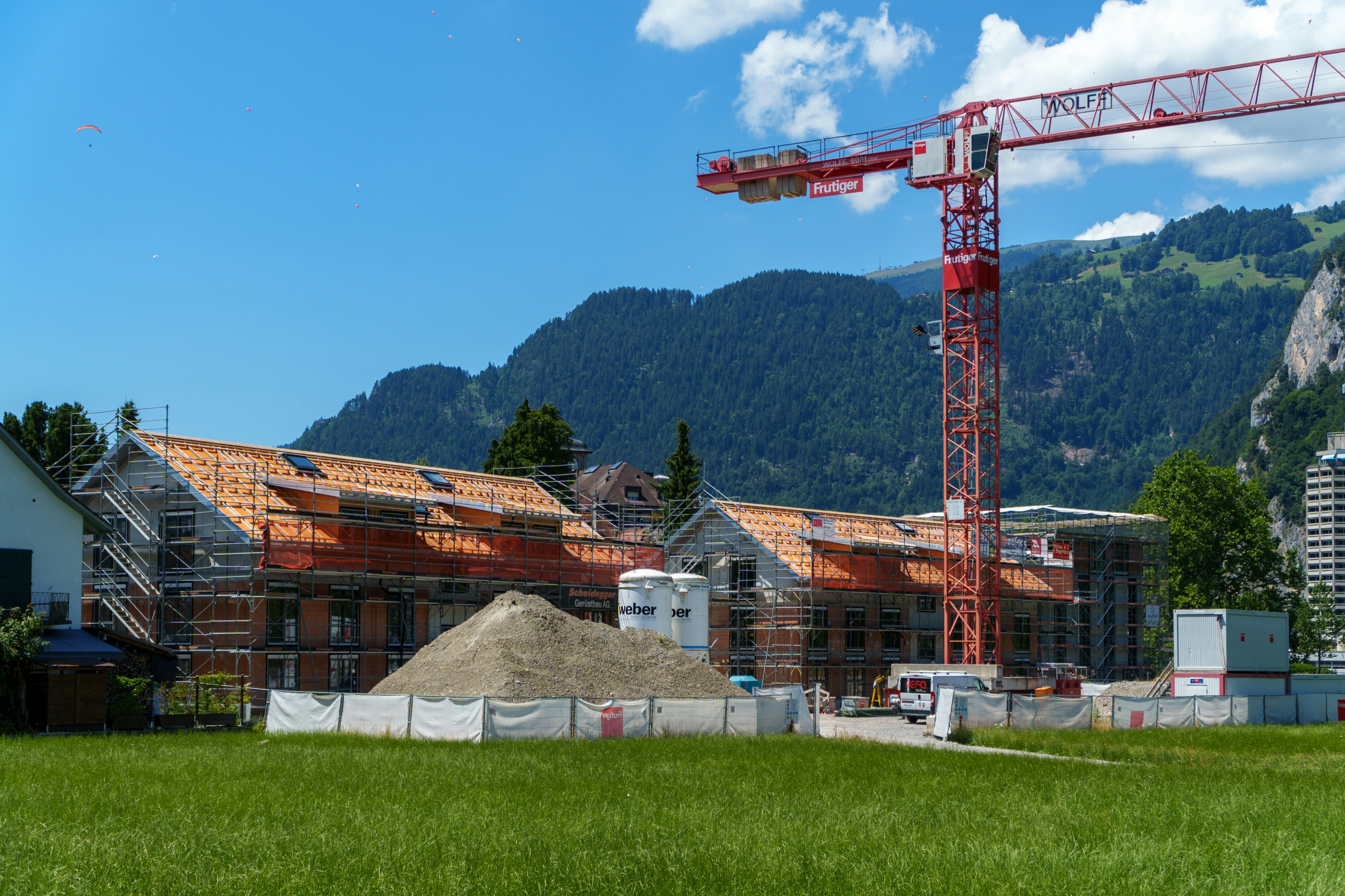 2 Houses being built in front of a mountain. | Construction of houses is underway with a crane.