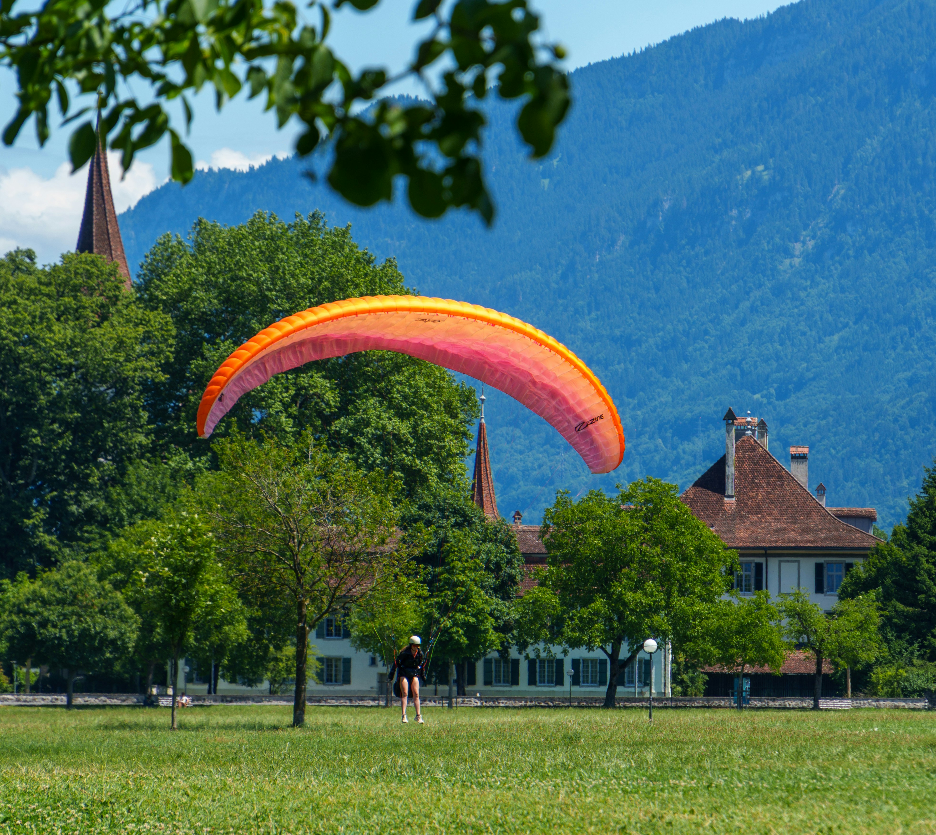 Orange-Pink Paraglider Arches Over a Sunlit European Parkfront