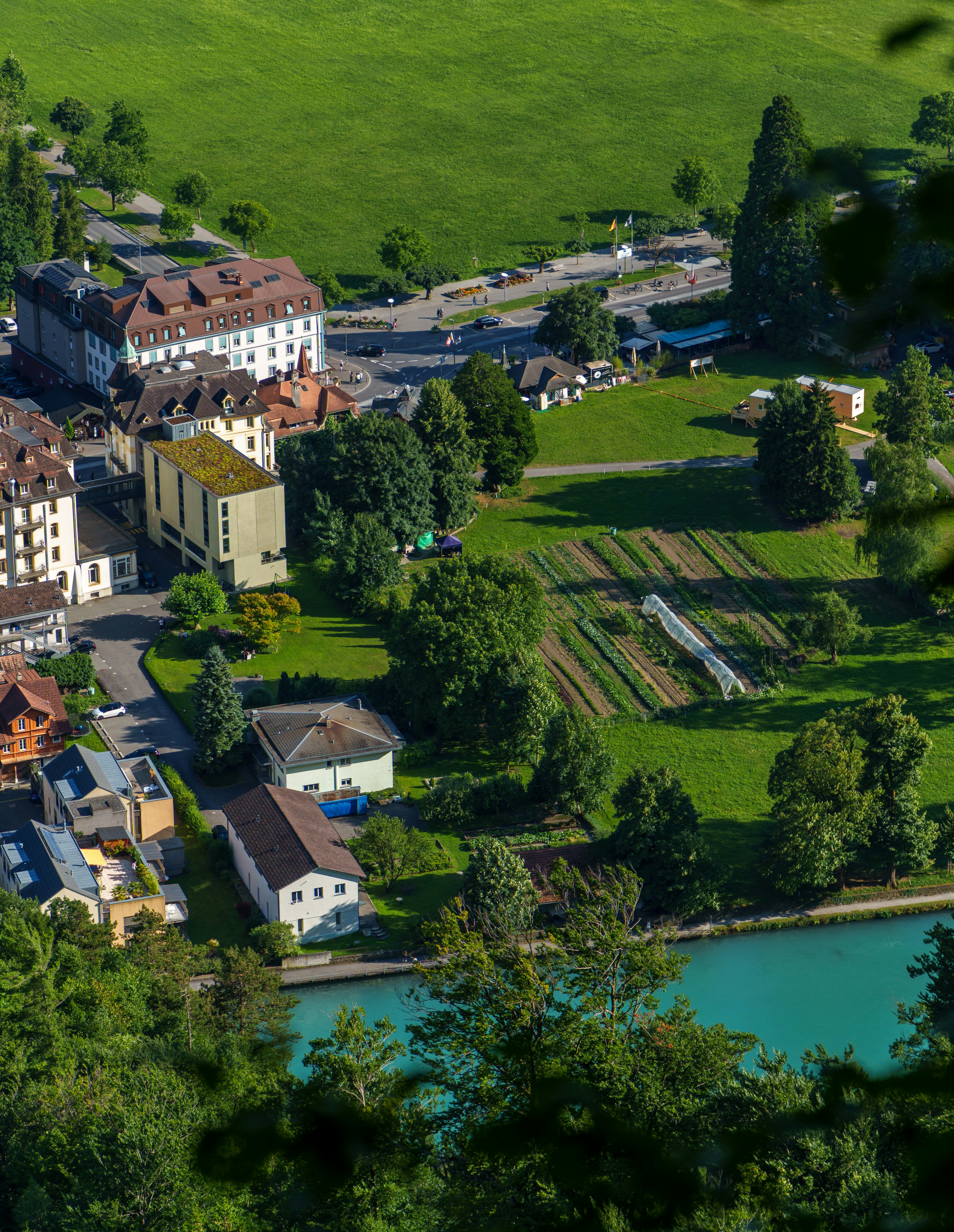 A small allotment on the edge of a swiss town by a glacial river. | A scenic view of a village and a river.