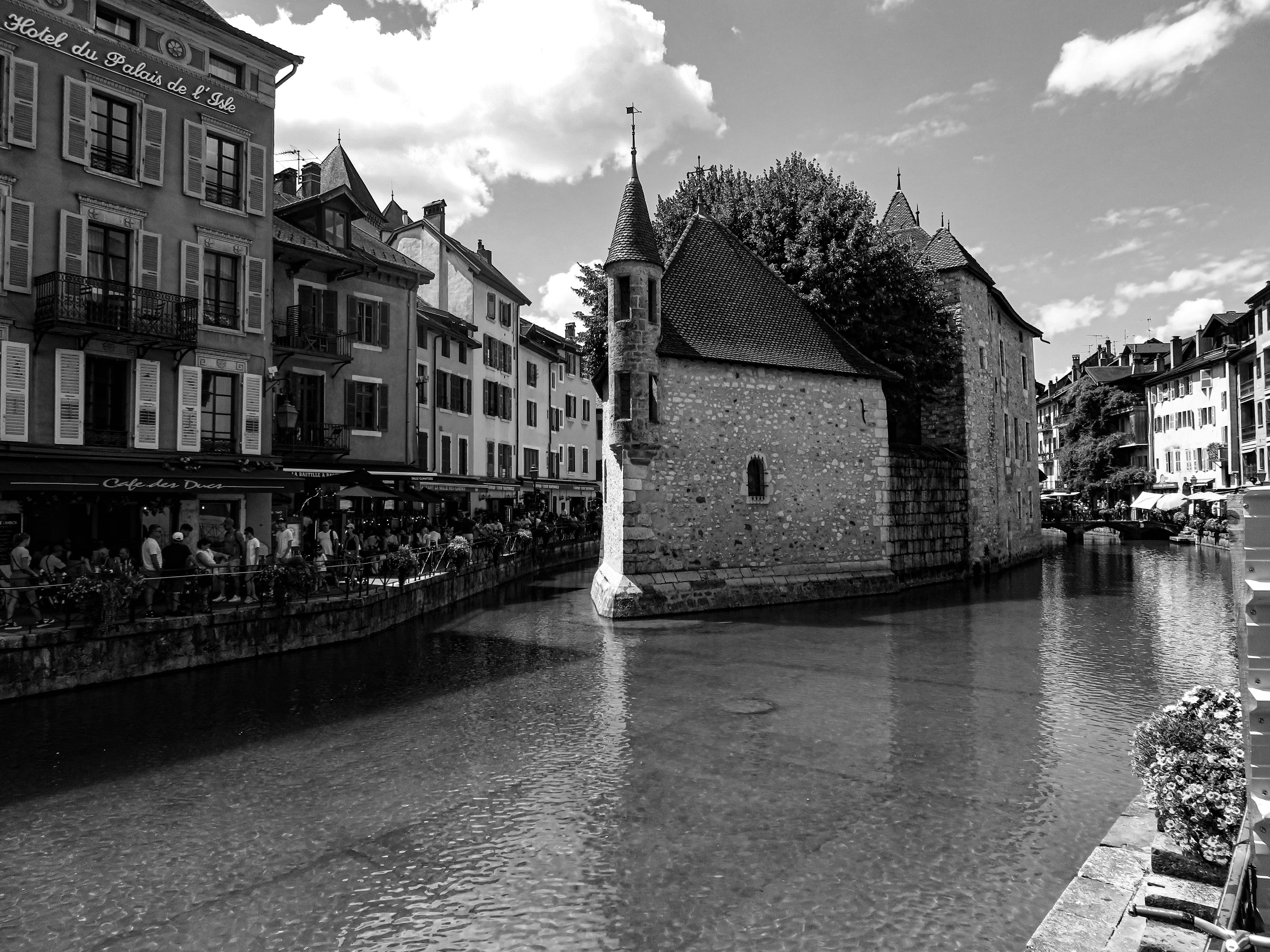 Historic stone building along a serene canal, flanked by charming architecture and vibrant outdoor dining areas. The scene captures a blend of nature and urban life.