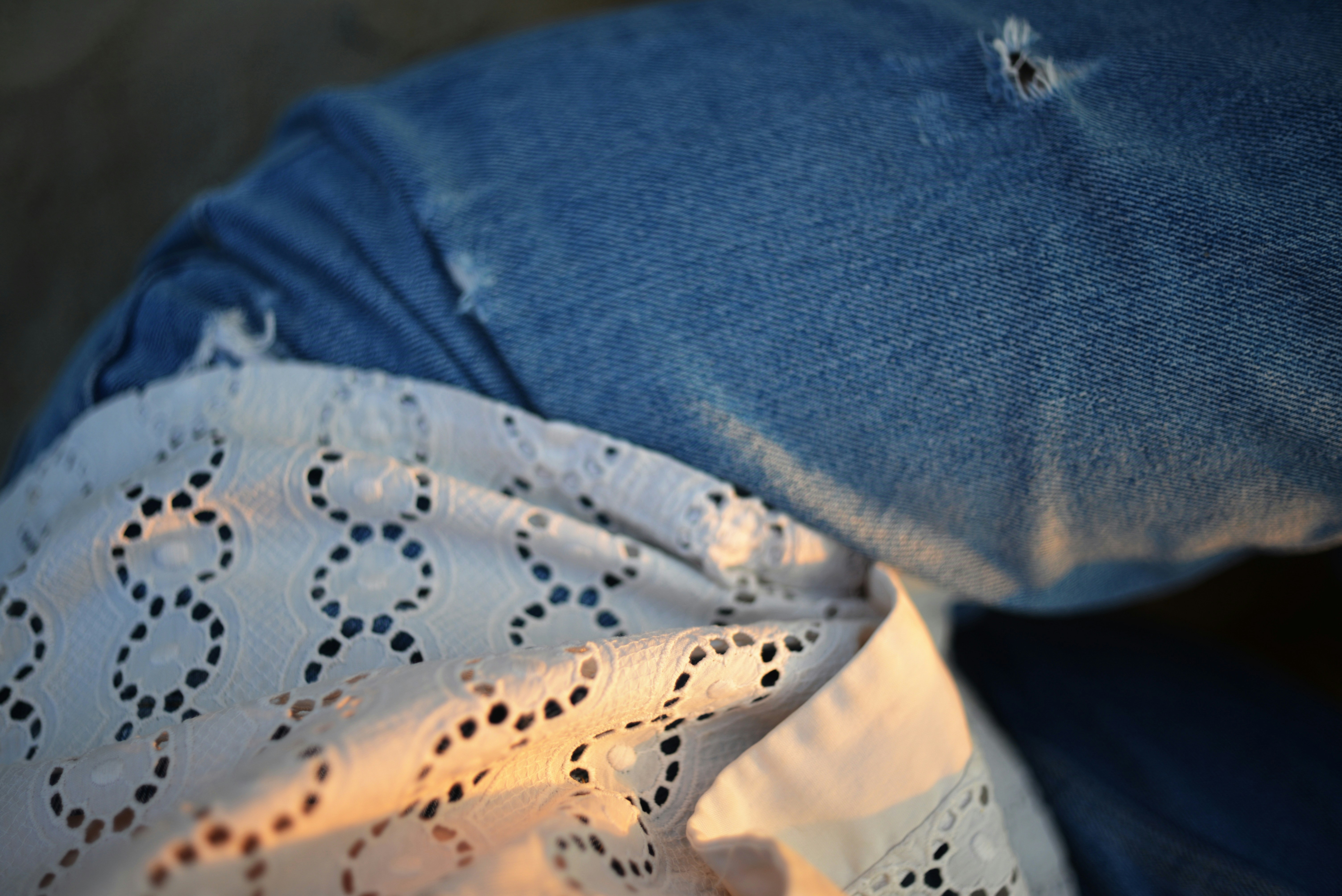 Close-up of denim and lace fabric, showcasing intricate patterns and textures illuminated by soft light.