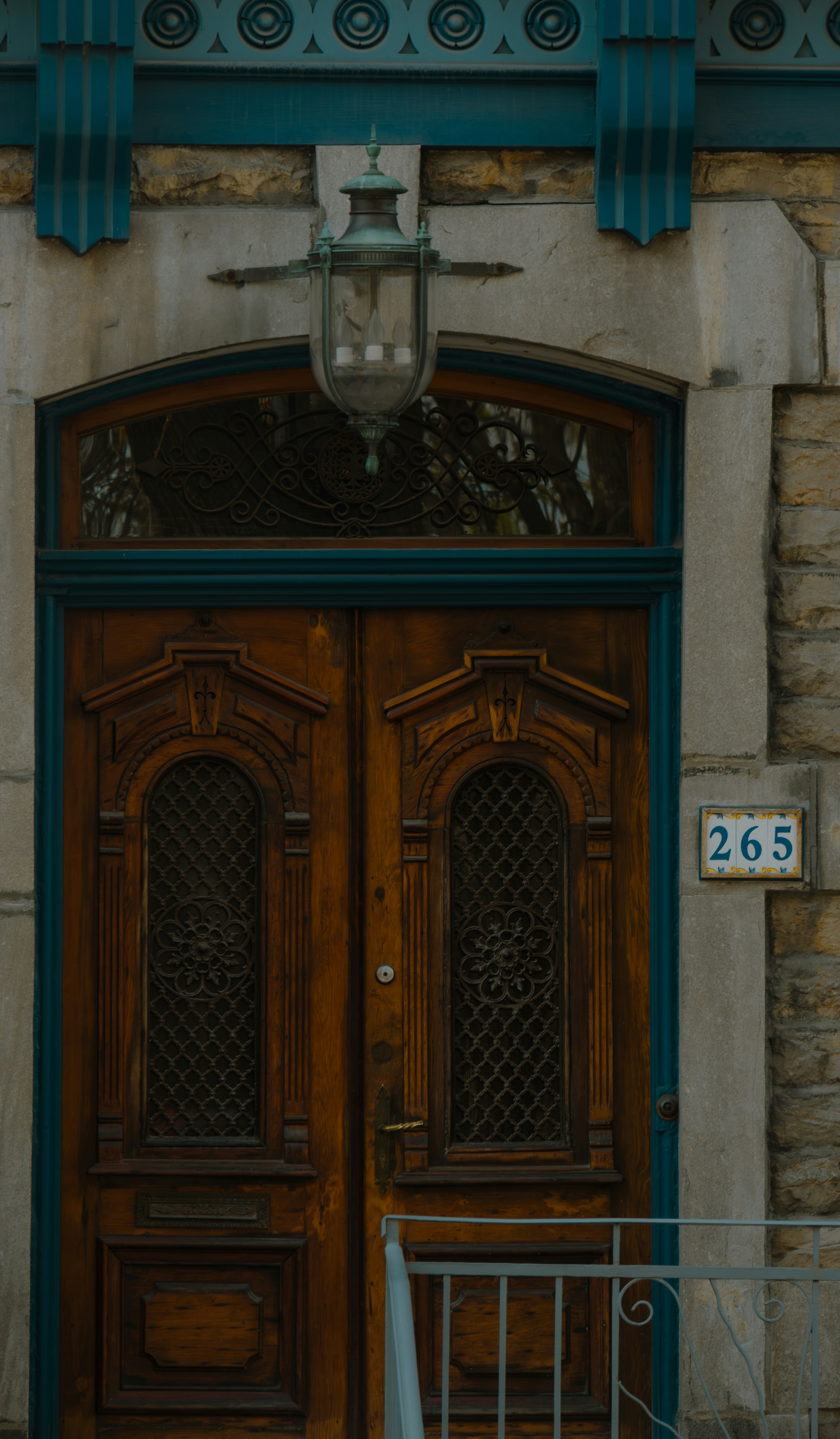 Intricately carved wooden double doors framed by a stone facade and an elegant lantern, featuring the number 265 prominently displayed.