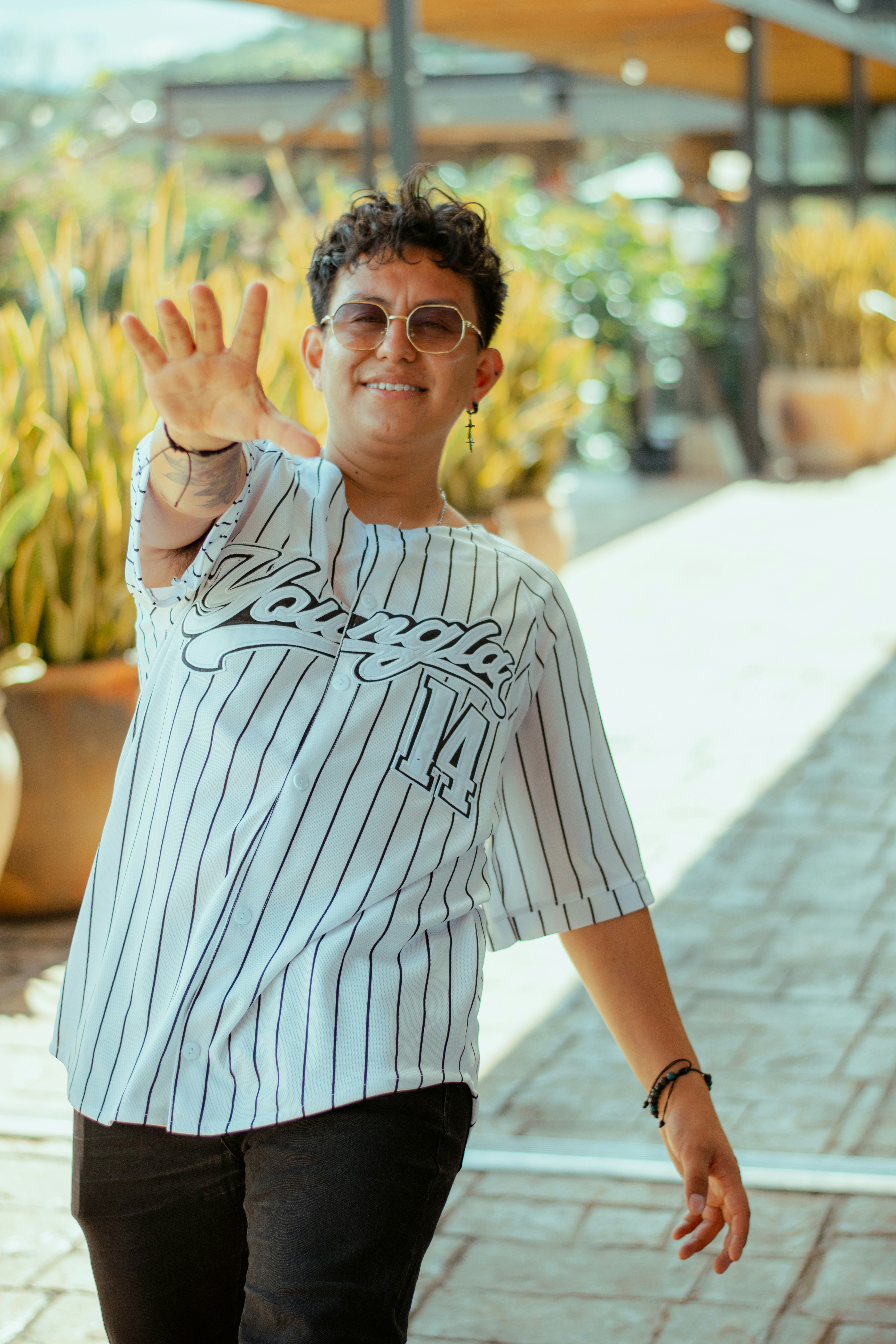 Forward Gesture in a Sunlit Plaza: Stripes, Sunglasses, and a Bright Moment