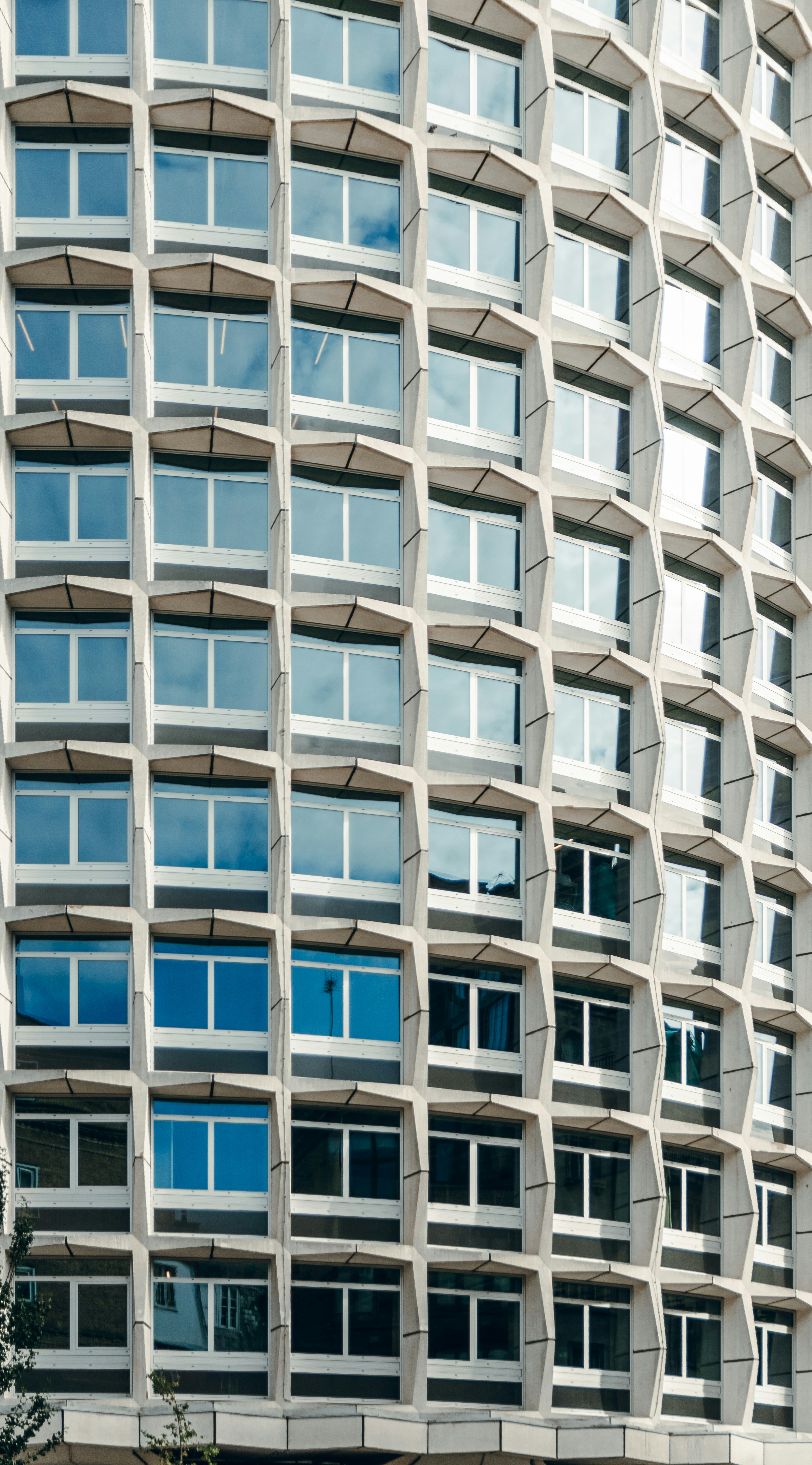 Intricate concrete structure featuring a rhythmic arrangement of windows reflecting the sky. The design emphasizes modern architectural aesthetics.