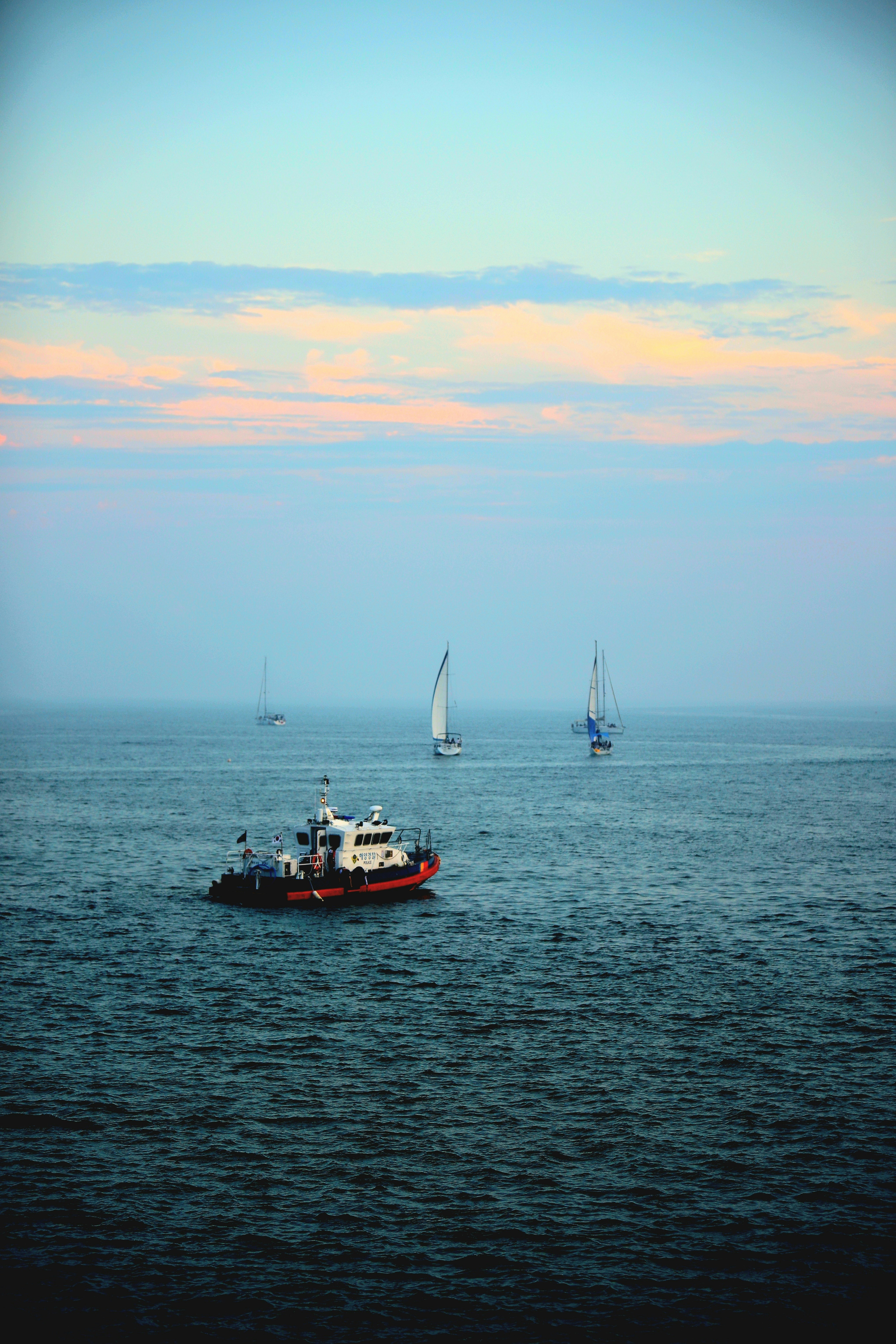 A vibrant scene of a motorboat surrounded by sailboats gliding across calm waters under a pastel sky.