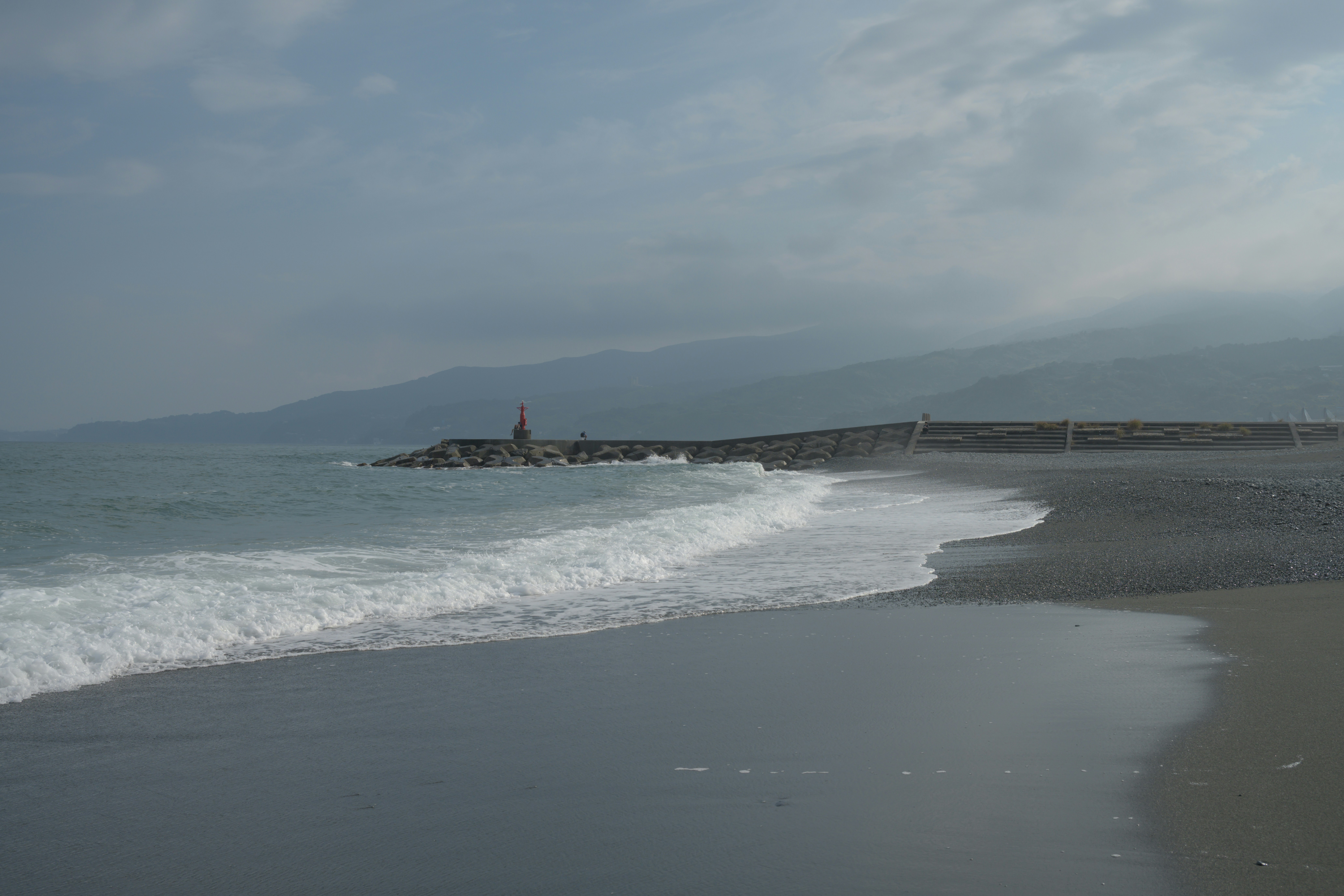 Waves crash onto the beach near a breakwater.