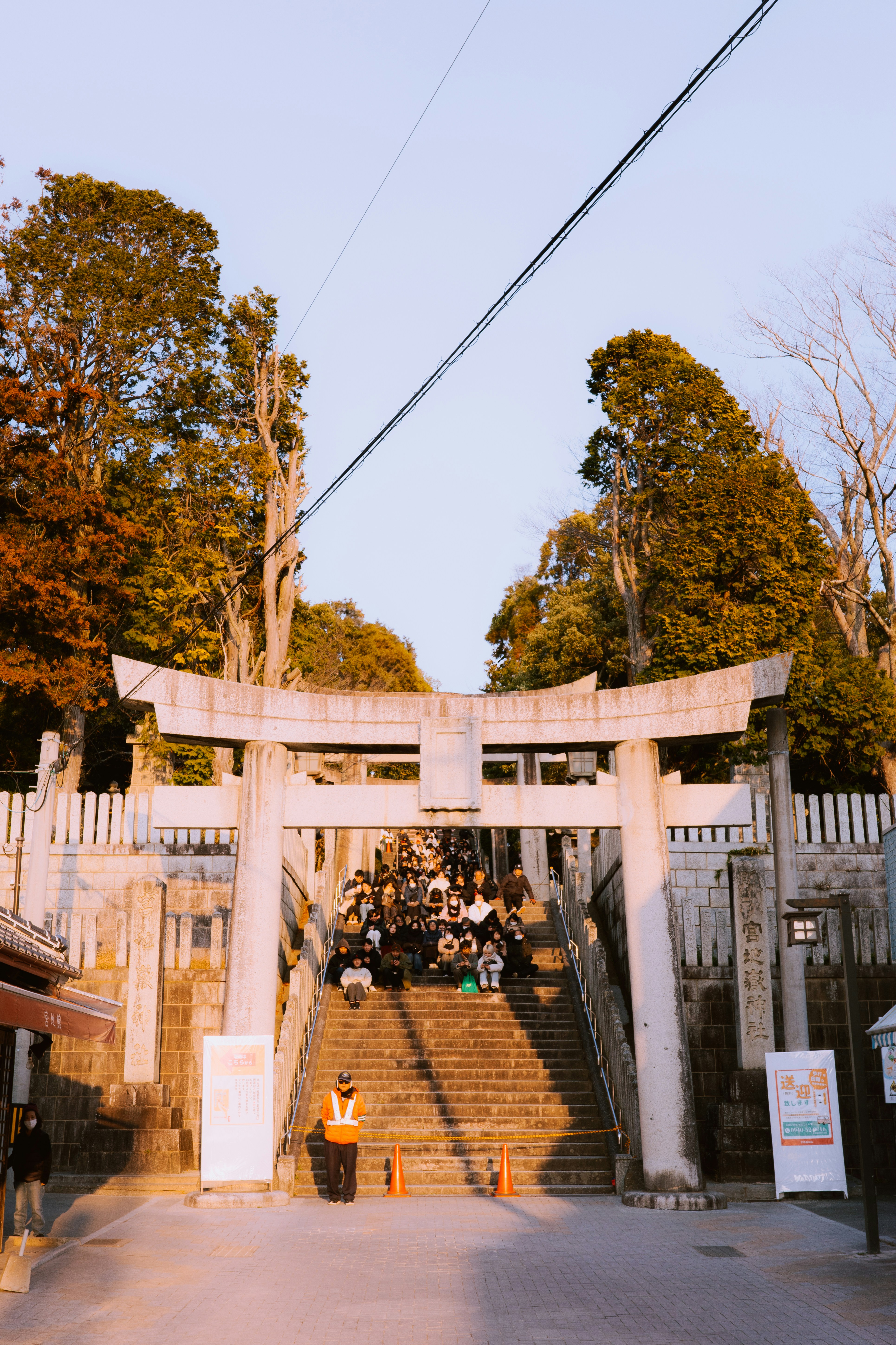 A traditional torii gate frames a staircase leading to a serene destination, with visitors gathered on the steps. The warm light casts a tranquil ambiance.