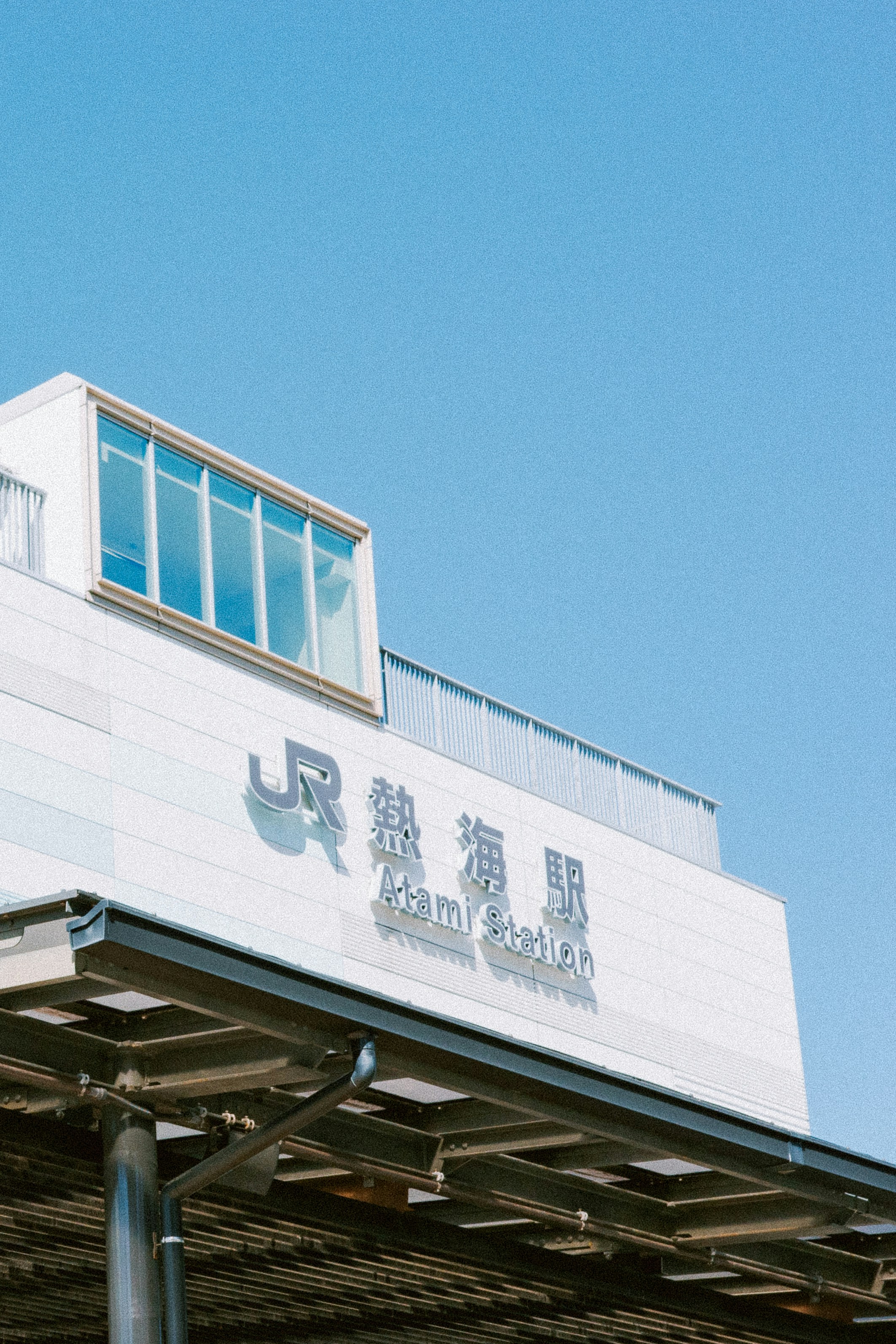 Here's a caption for the image: **the atami station sign under a clear ...