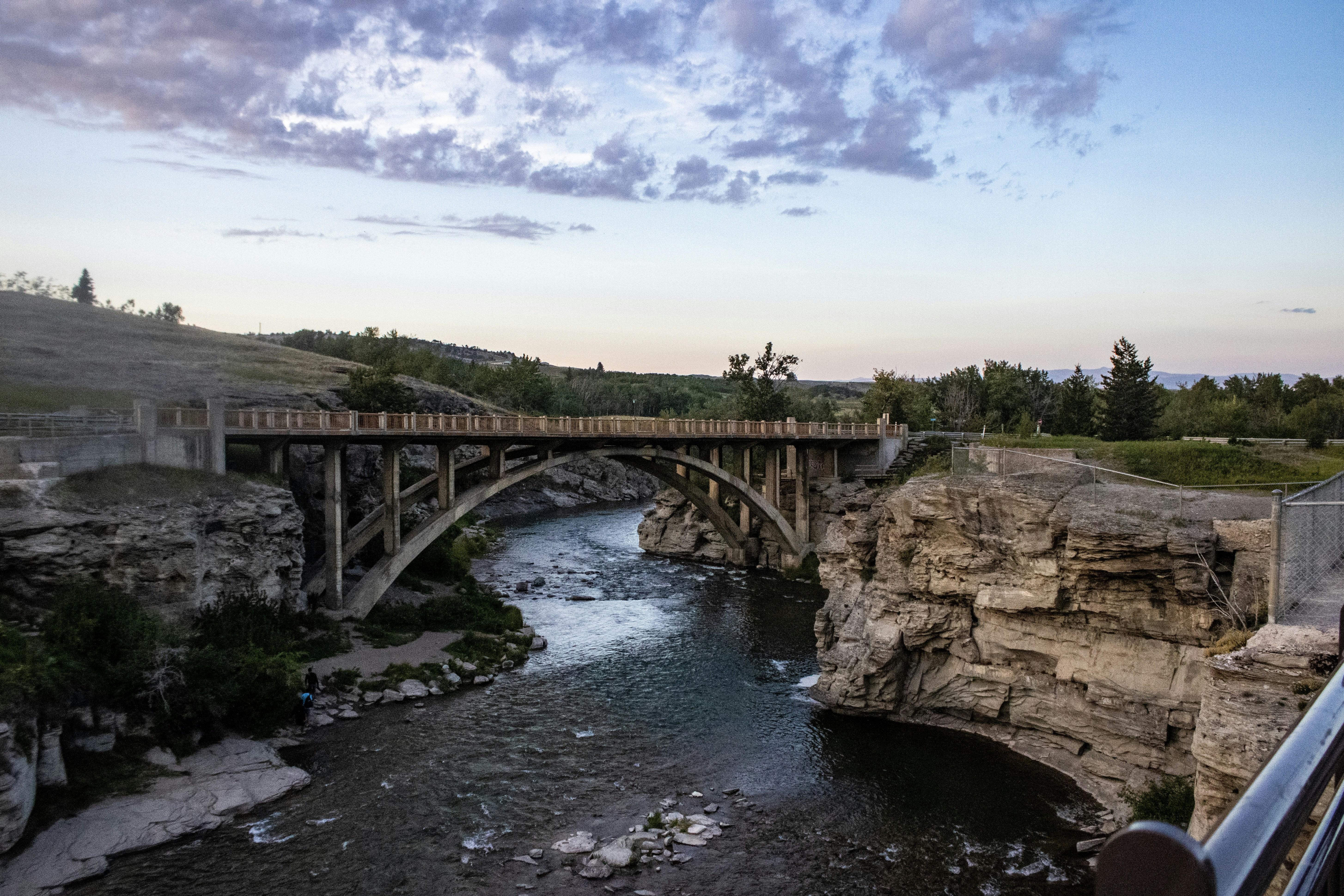 Mountain river flowing under a bridge. | A stone bridge arches over a flowing river.