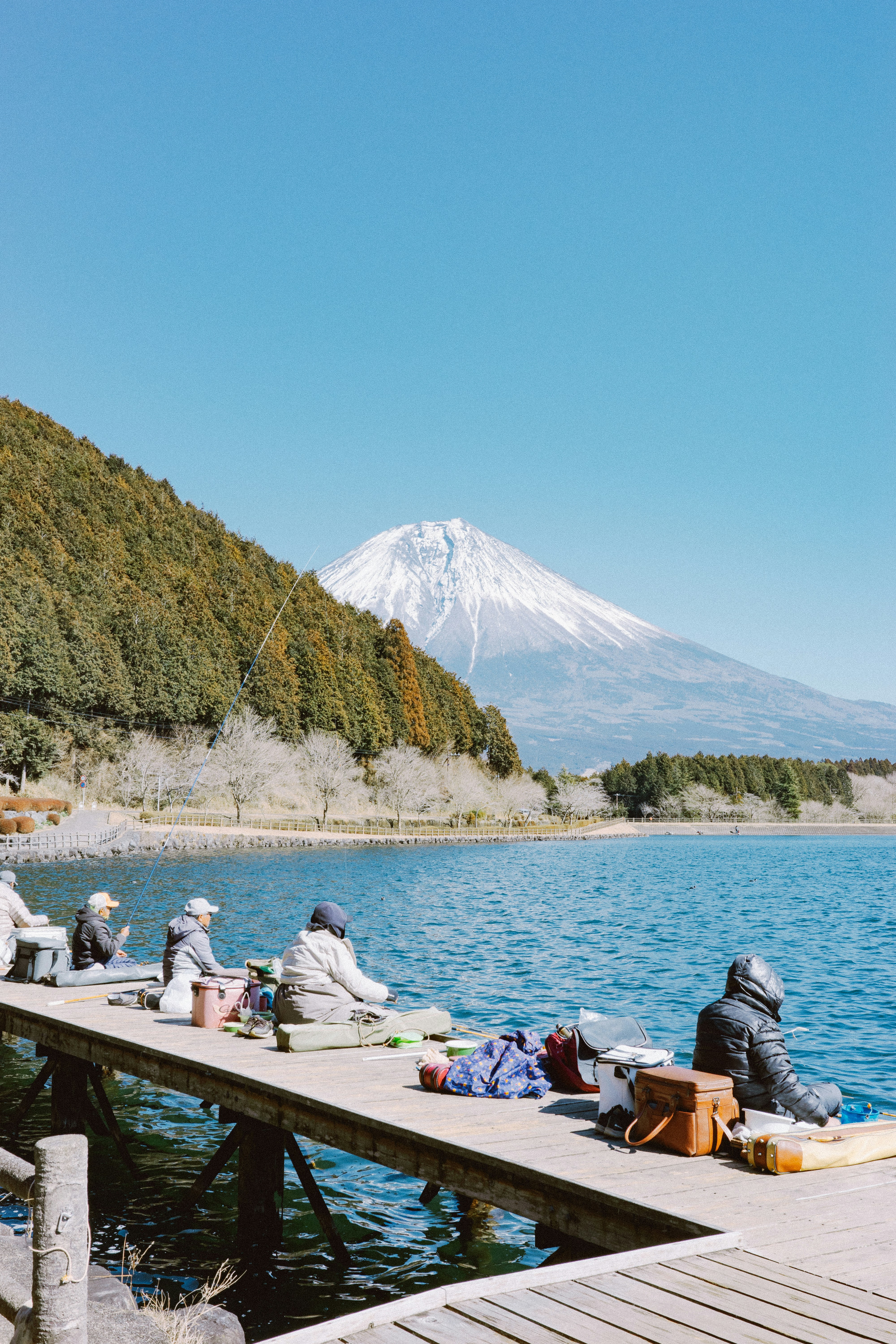 People fish by a lake with mount fuji.