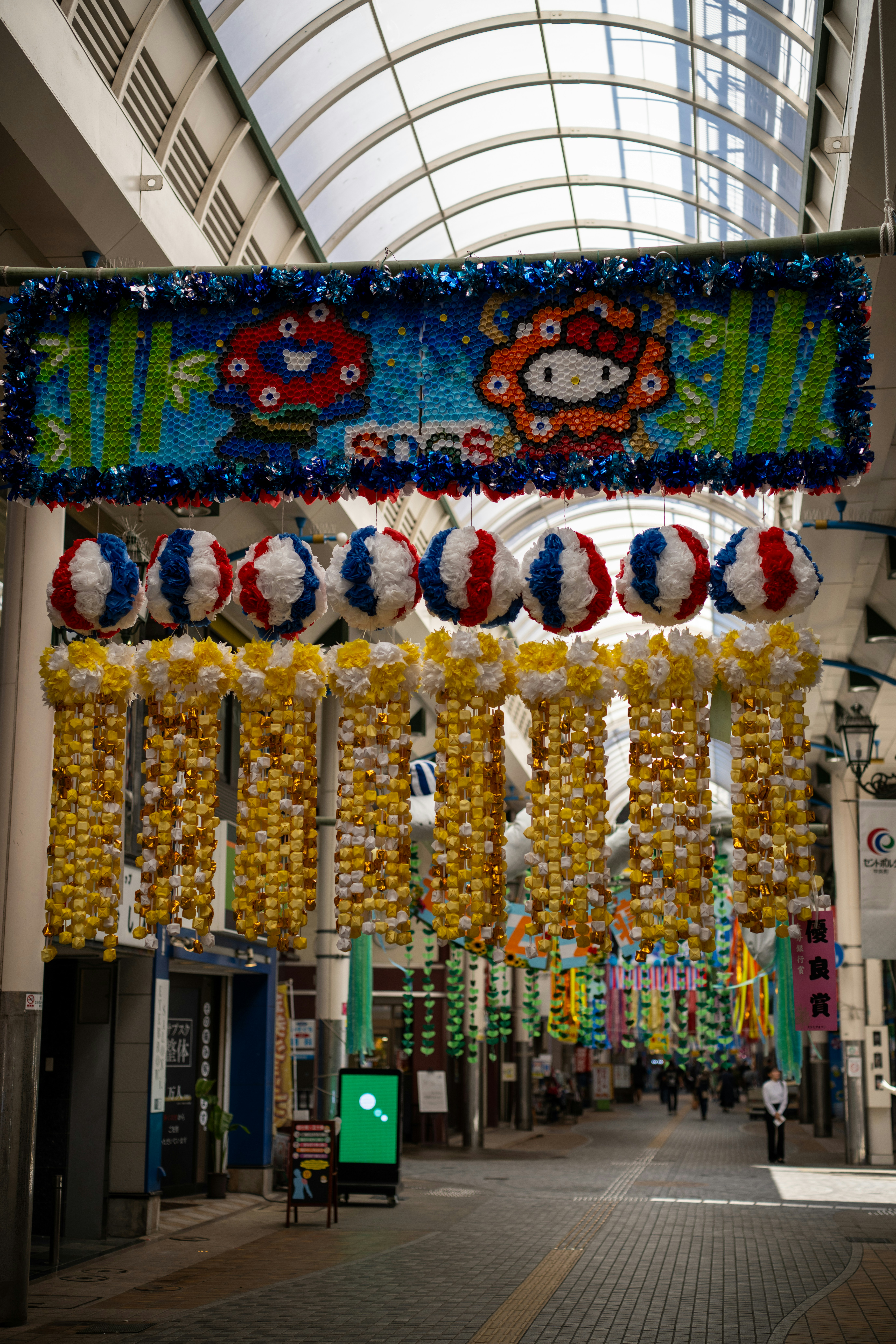 Festive decorations hang in a sunny shopping arcade.