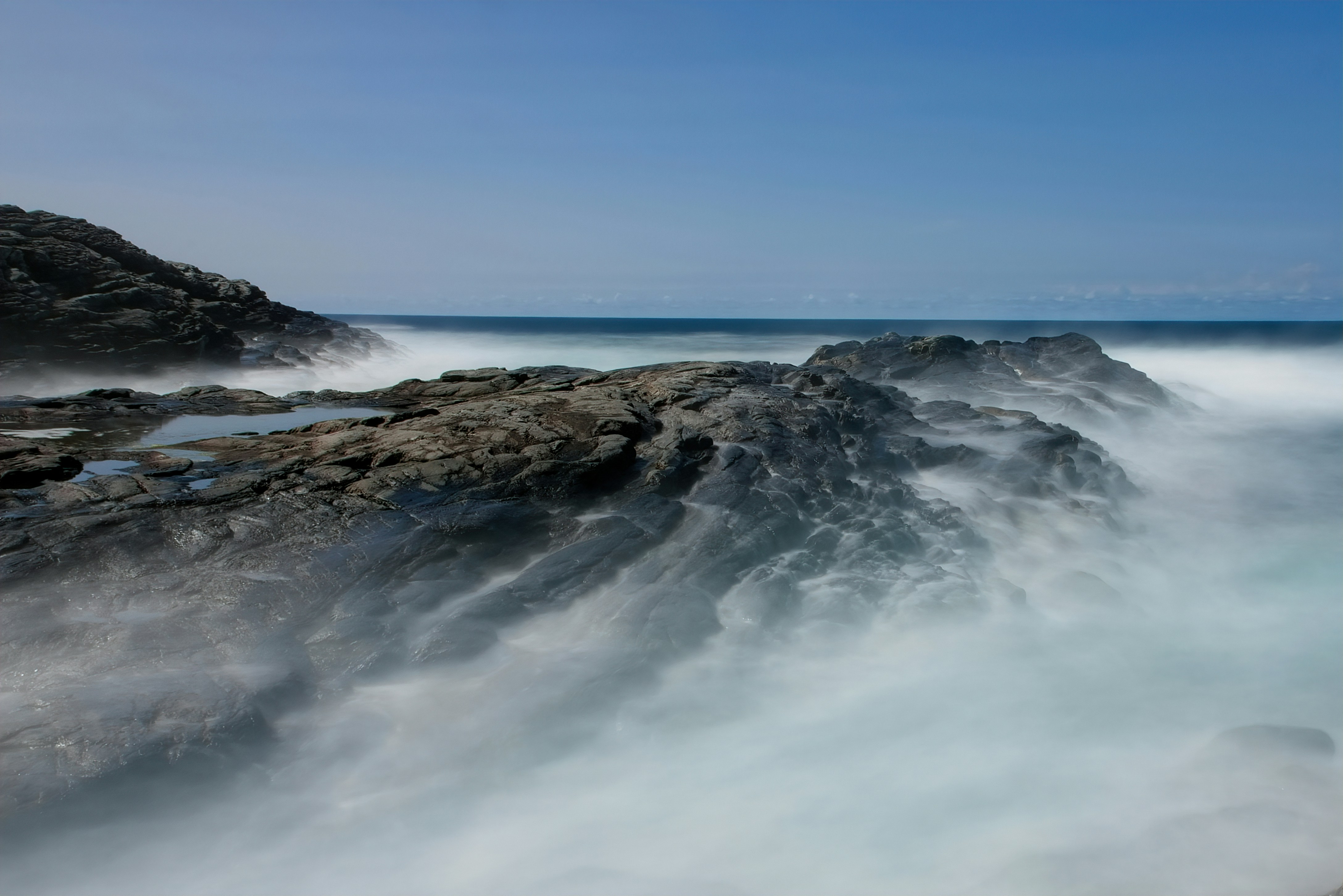 Big wave. | Waves crash against rocks under a clear sky.
