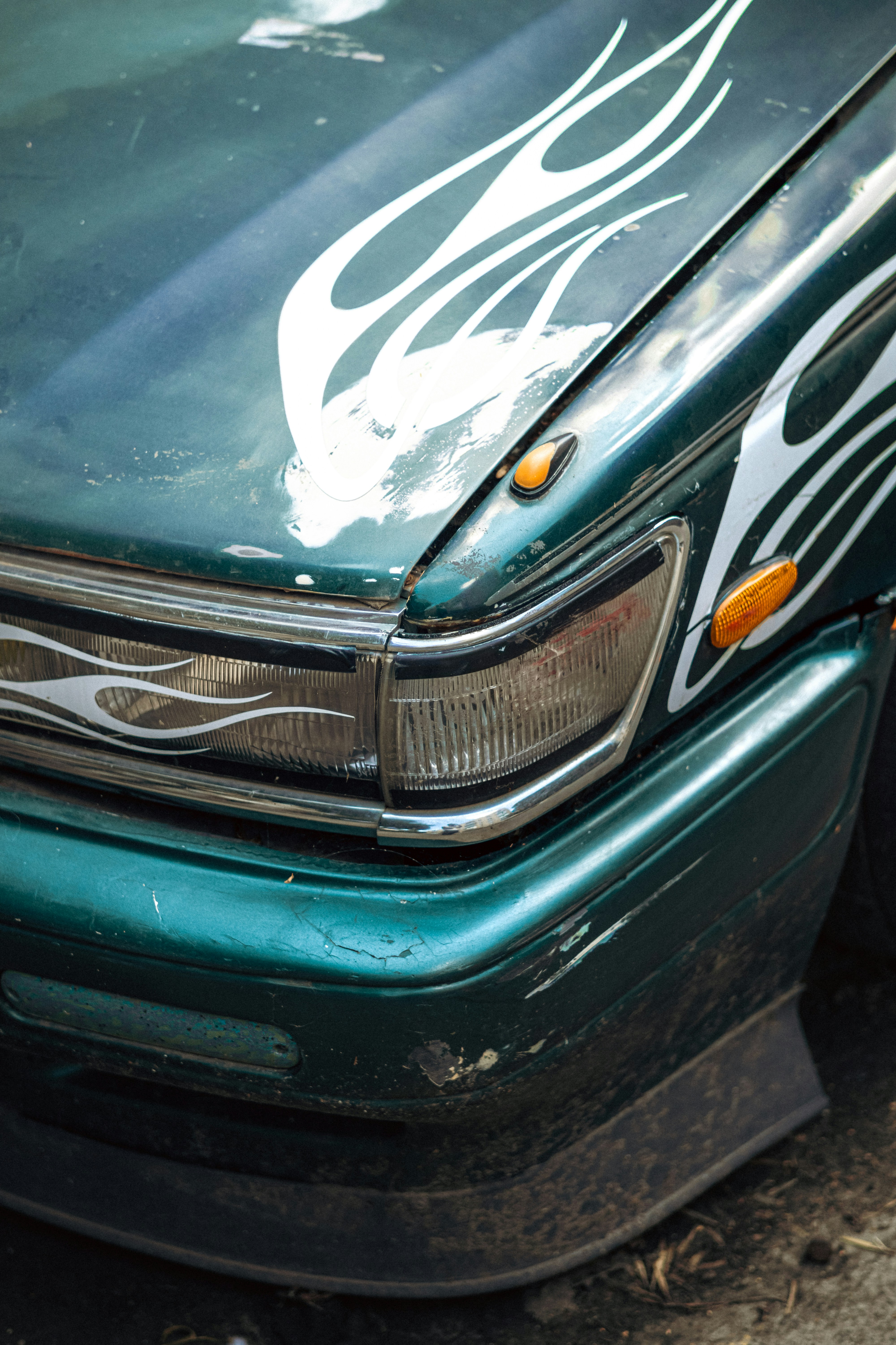 Close-up of a weathered car hood adorned with flame graphics and a tarnished headlight, showcasing the beauty of vintage automotive design.