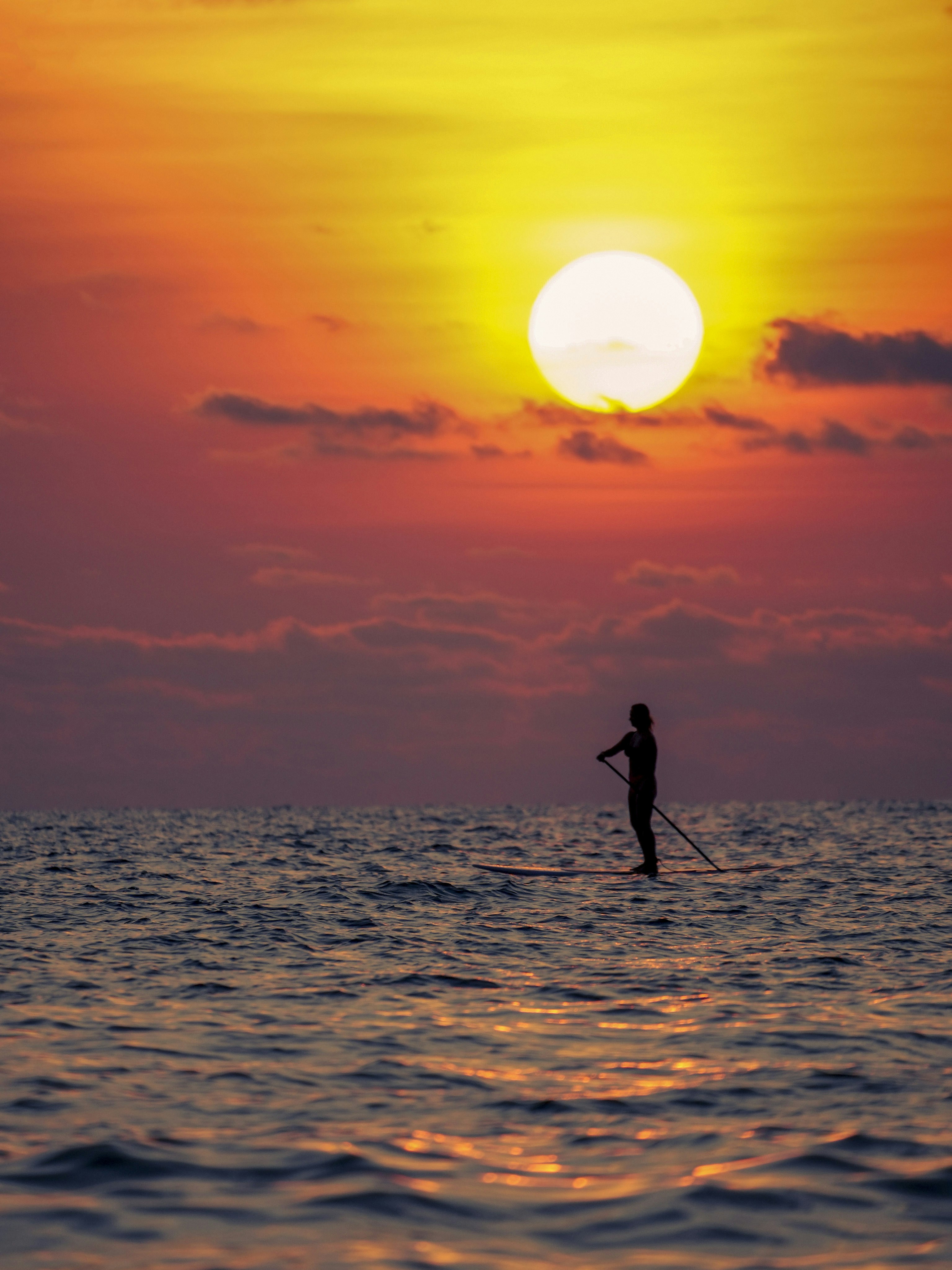 Woman on a SUP board at sunset | Paddleboarder enjoys a stunning sunset on the ocean.