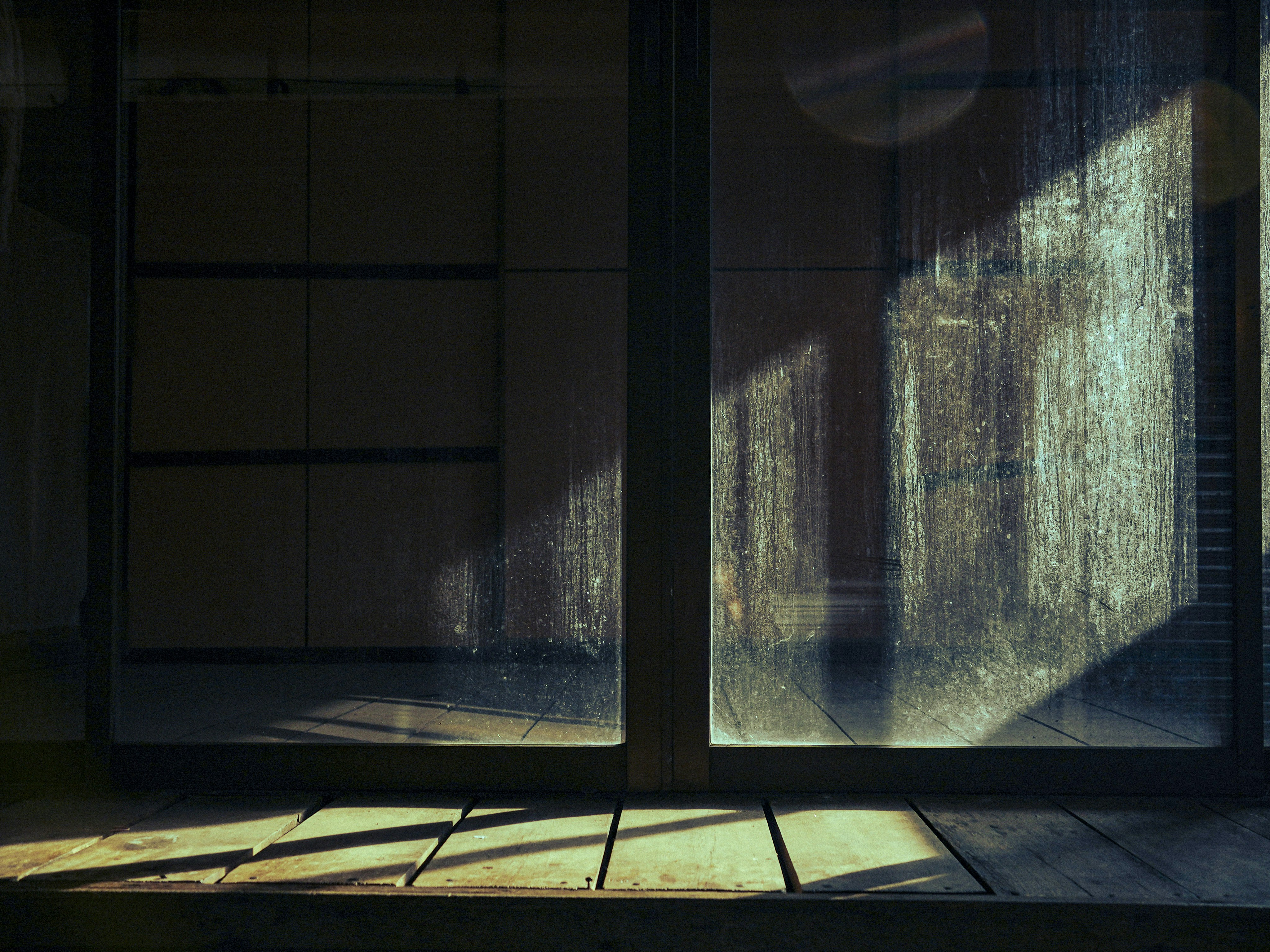 Play of light and shadow on dirty window | Sunlight streams through a glass door and onto wooden planks.