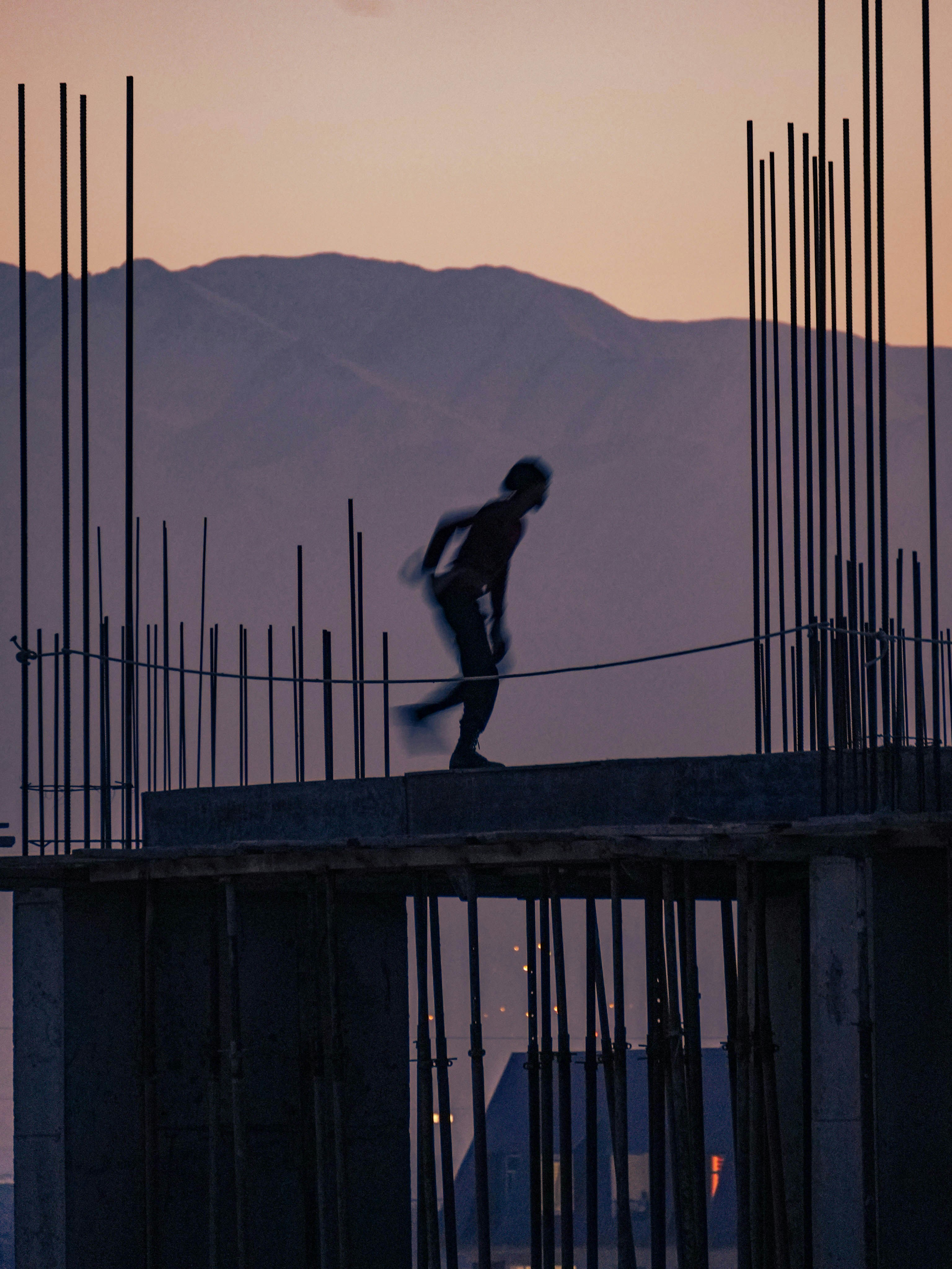 Silhouette of a figure balancing atop a construction site against a backdrop of mountains at twilight.