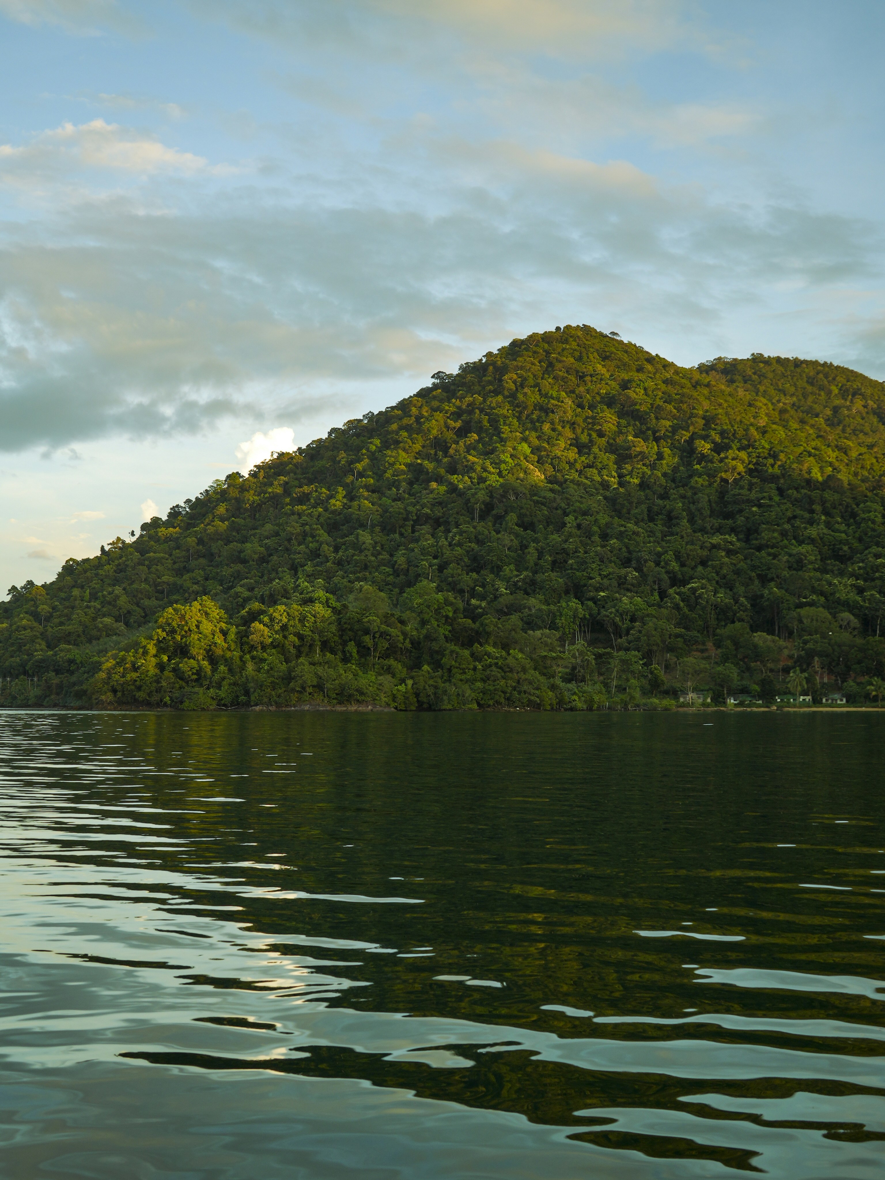 Lush green mountain rising above calm waters, reflecting the serene landscape under a softly lit sky.
