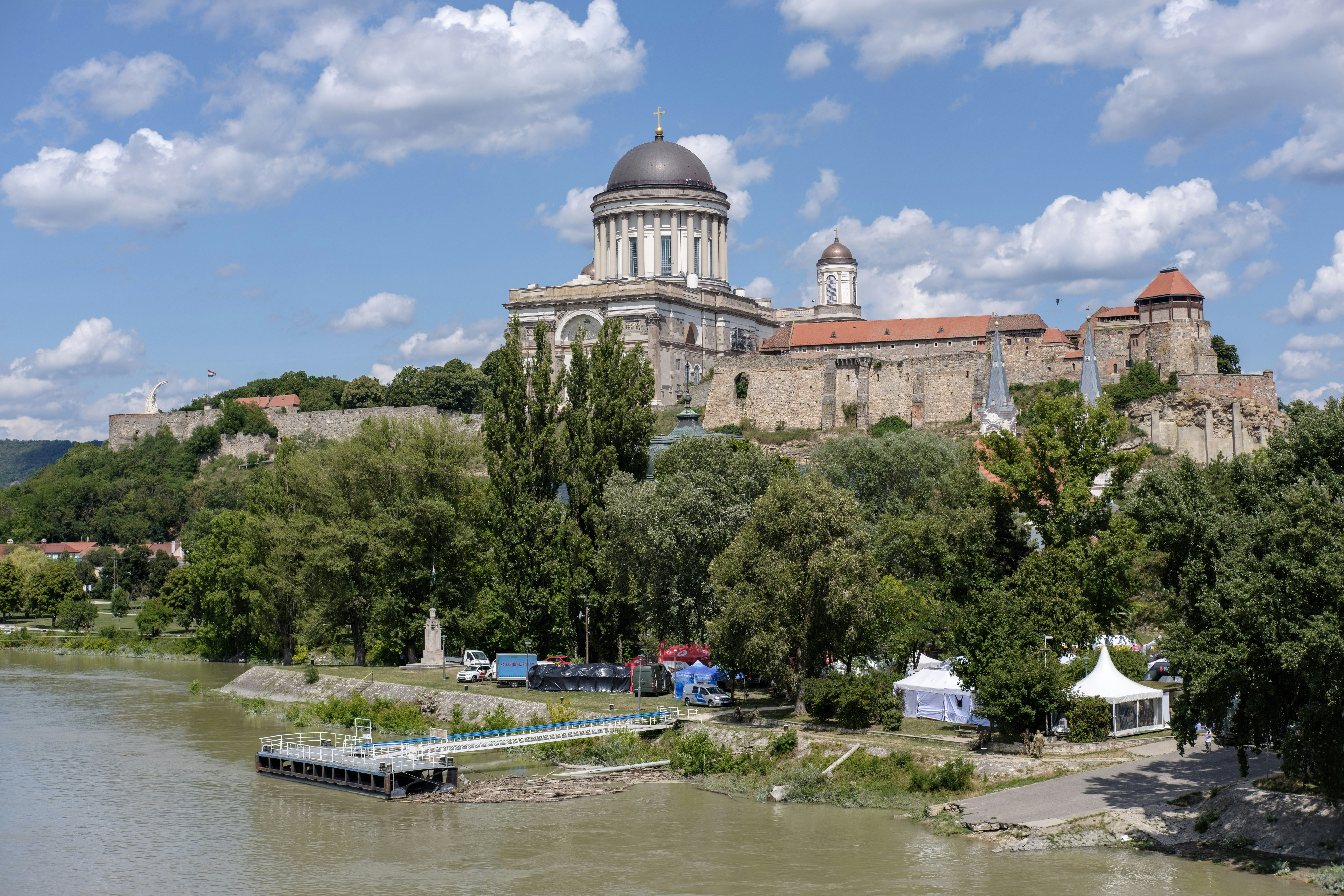 Bazilika | A majestic building stands on a hill by the river.