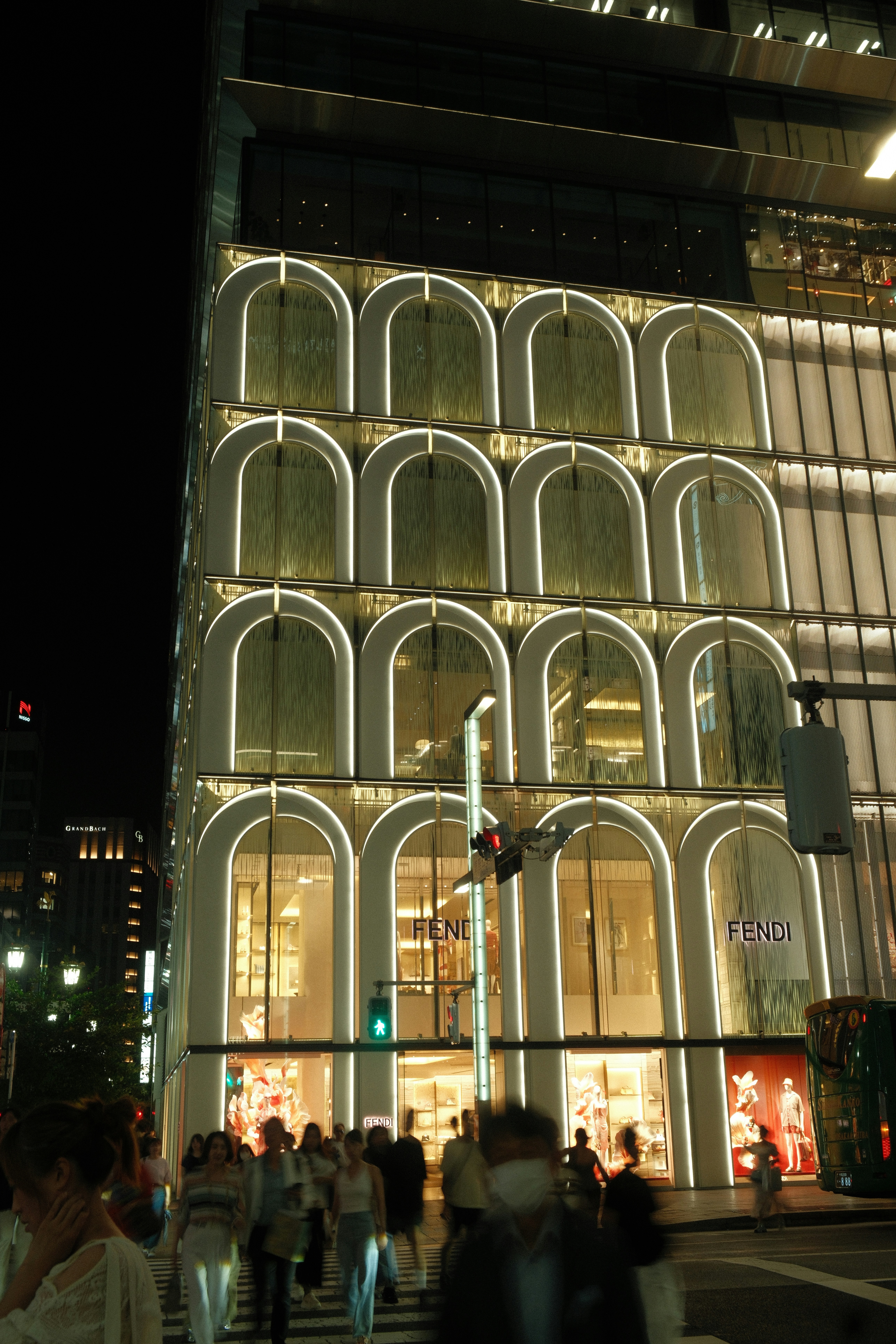 Architectural façade of a Fendi store illuminated by intricate lighting at night, with pedestrians crossing the street below.