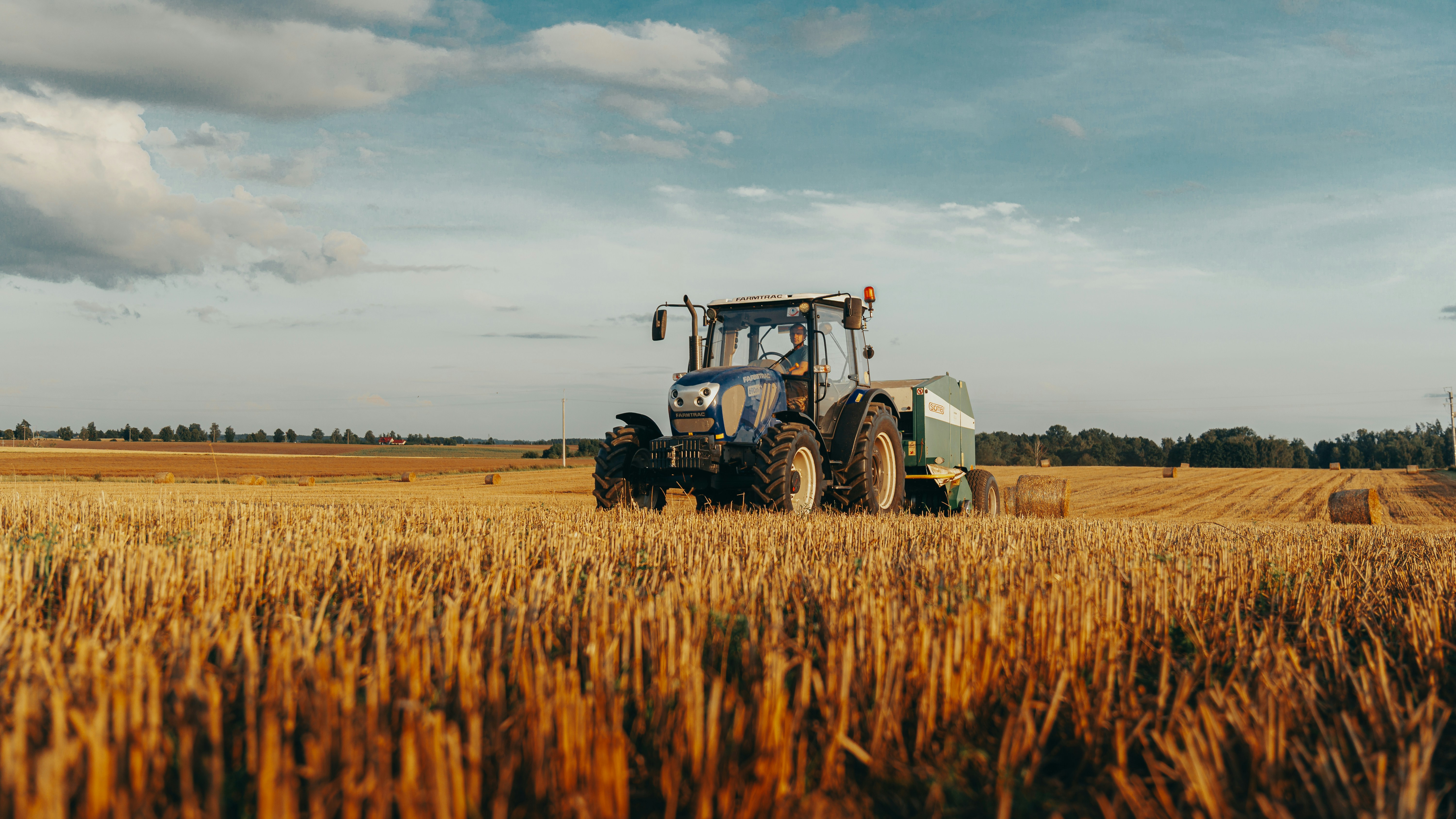 A blue tractor working through golden fields under a cloudy sky, showcasing the harmony of machinery and nature.
