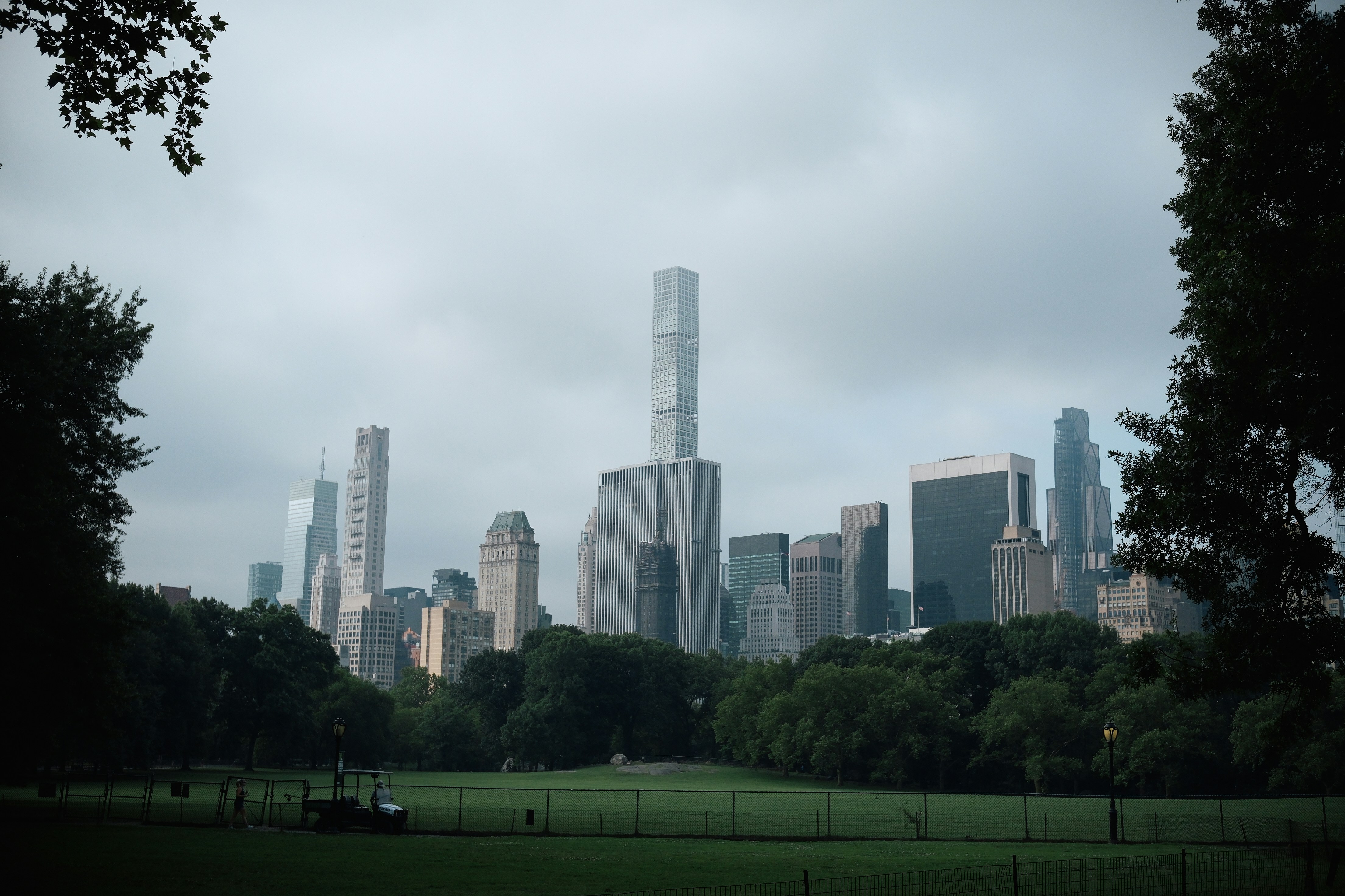 A panoramic view of a city skyline shrouded in soft, overcast skies, with lush greenery in the foreground. The image captures the juxtaposition of nature and urban architecture.