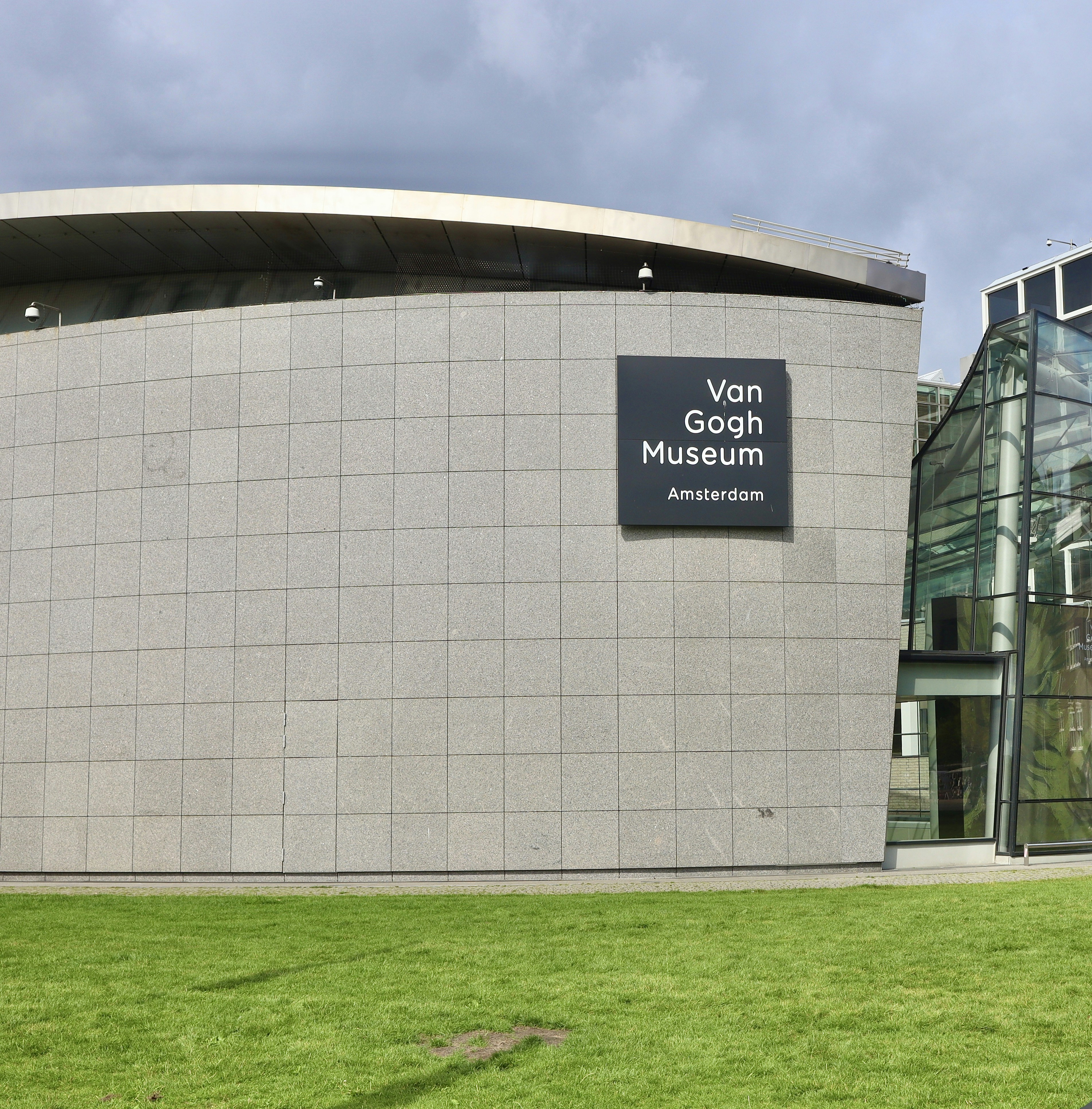 Modern architectural design of the Van Gogh Museum in Amsterdam, showcasing a blend of stone and glass elements. The museum's name is prominently displayed.