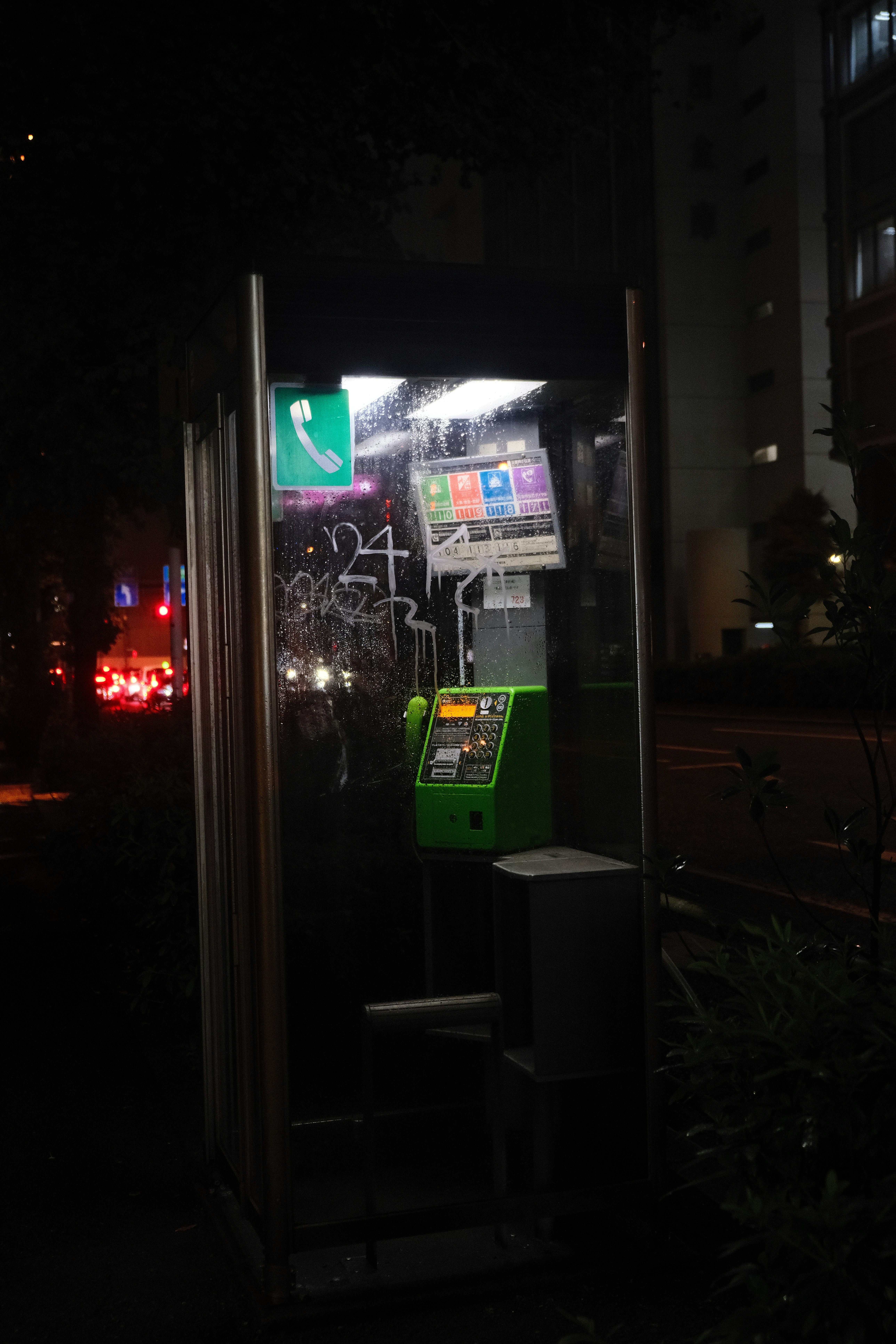 An illuminated phone booth stands at night.