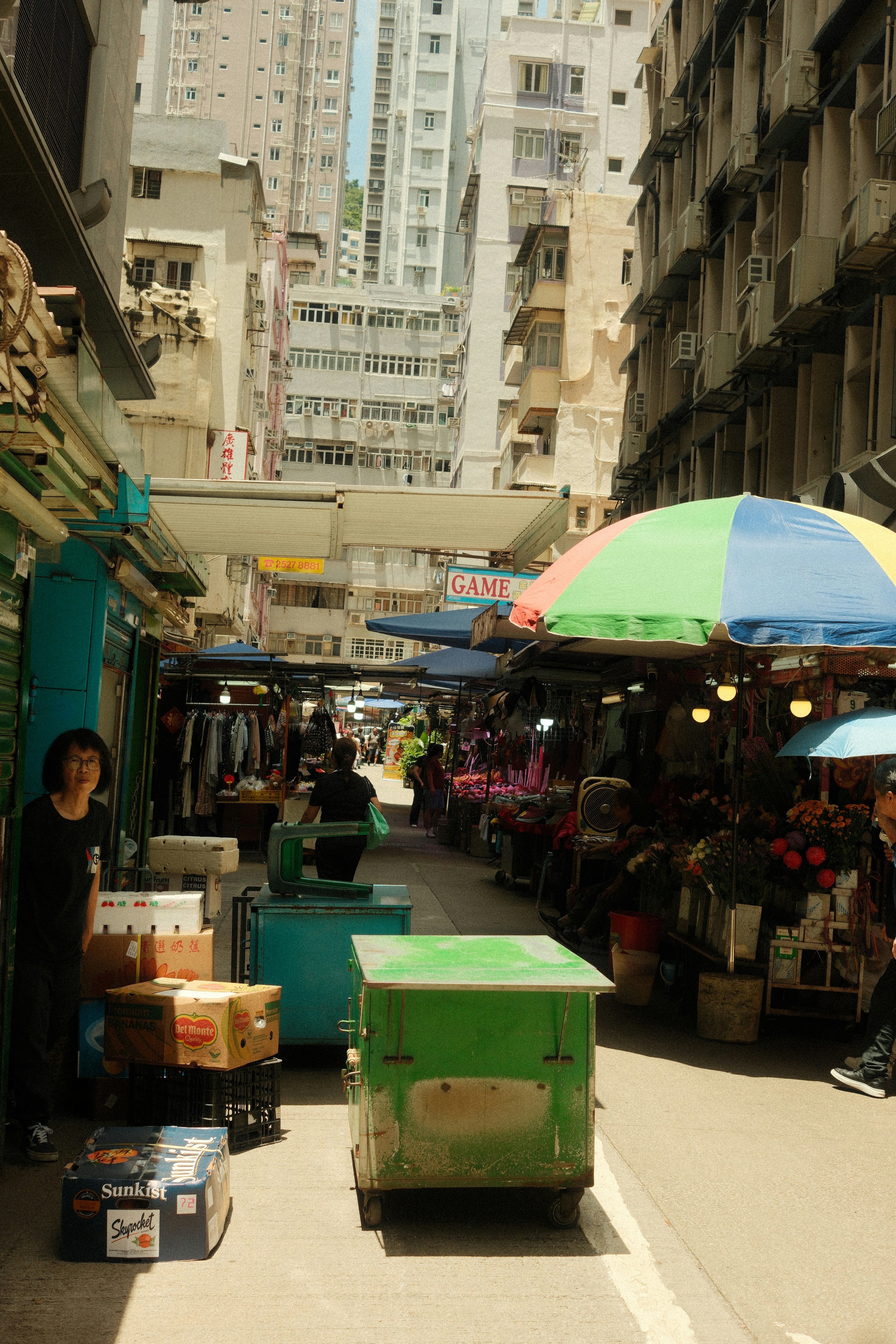 Vibrant street market scene with colorful umbrellas, showcasing local vendors and shoppers amidst towering urban buildings.