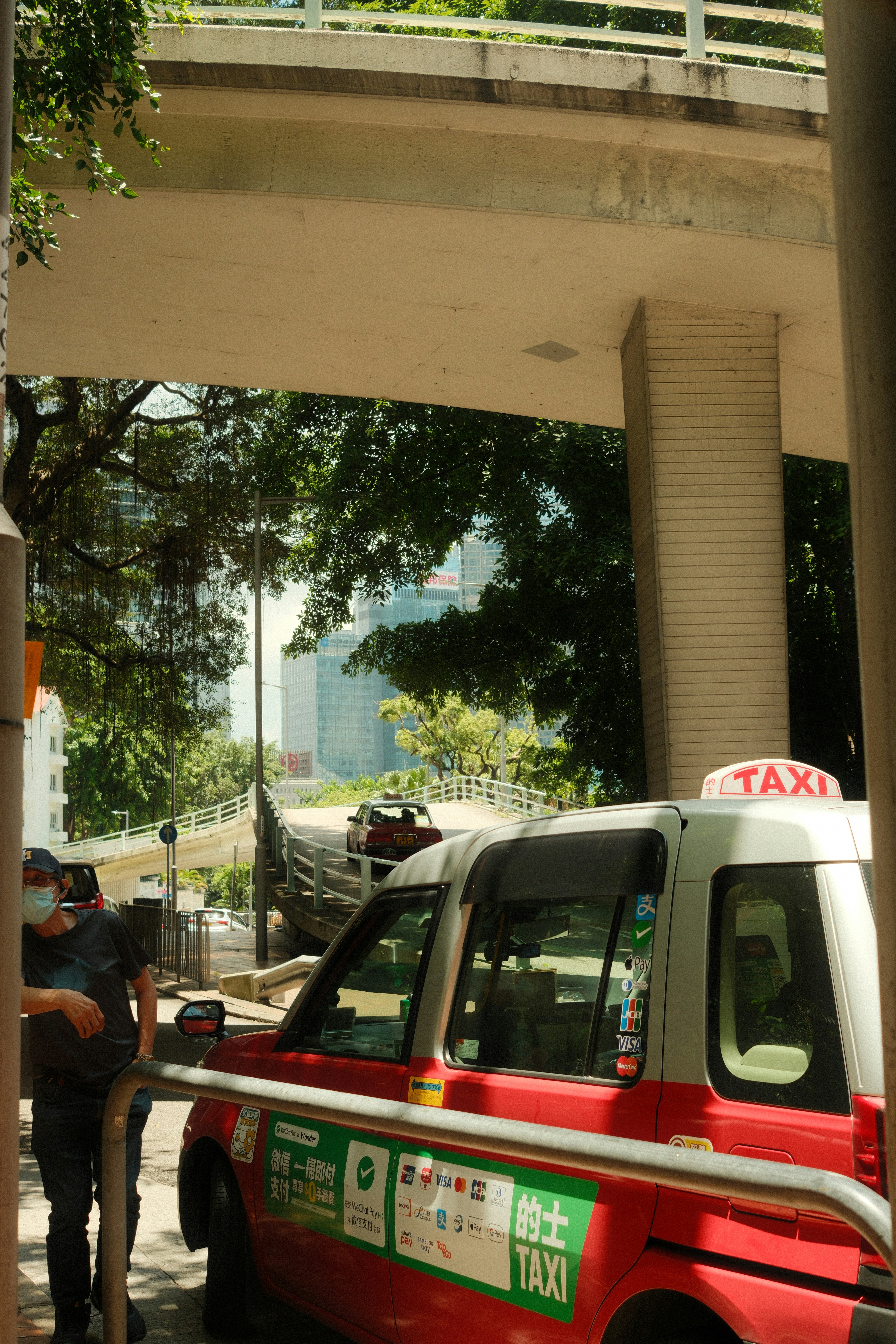 A hong kong taxi is parked under a bridge.
